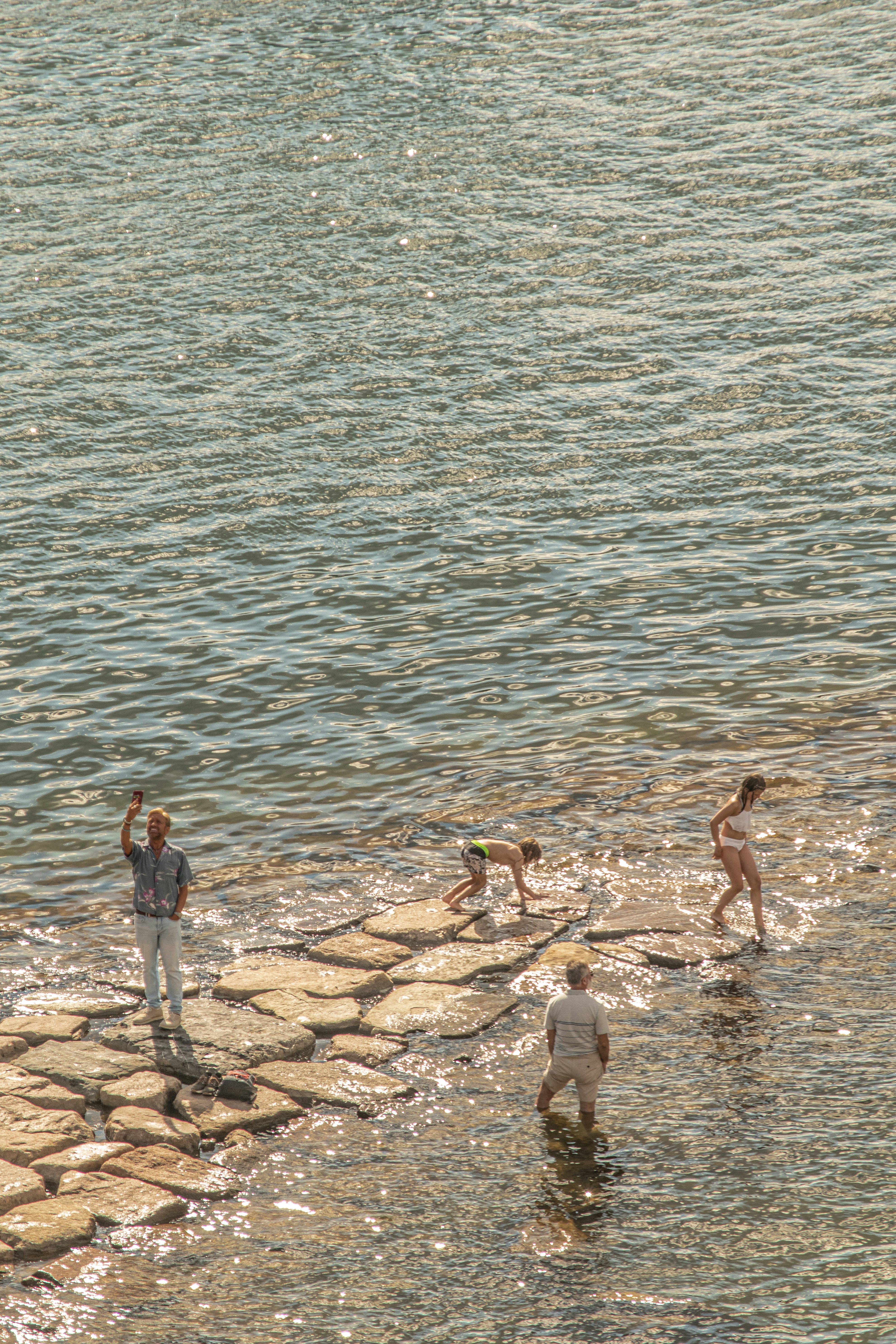 Family enjoying a sunny day by the water, exploring the rocky shoreline and playing in the shallows.