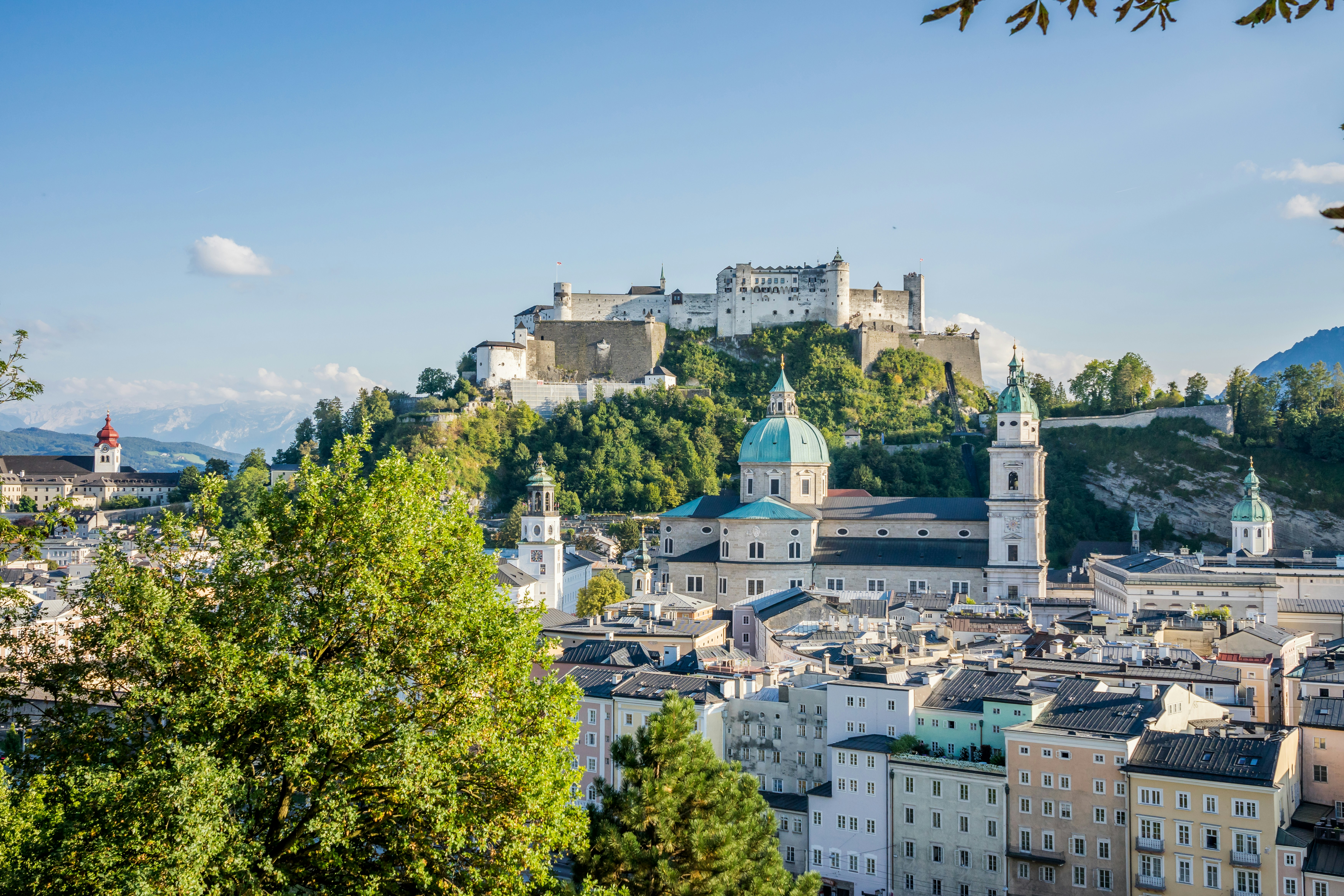 Historic fortress overlooking the city of Salzburg, framed by lush greenery and clear blue skies.