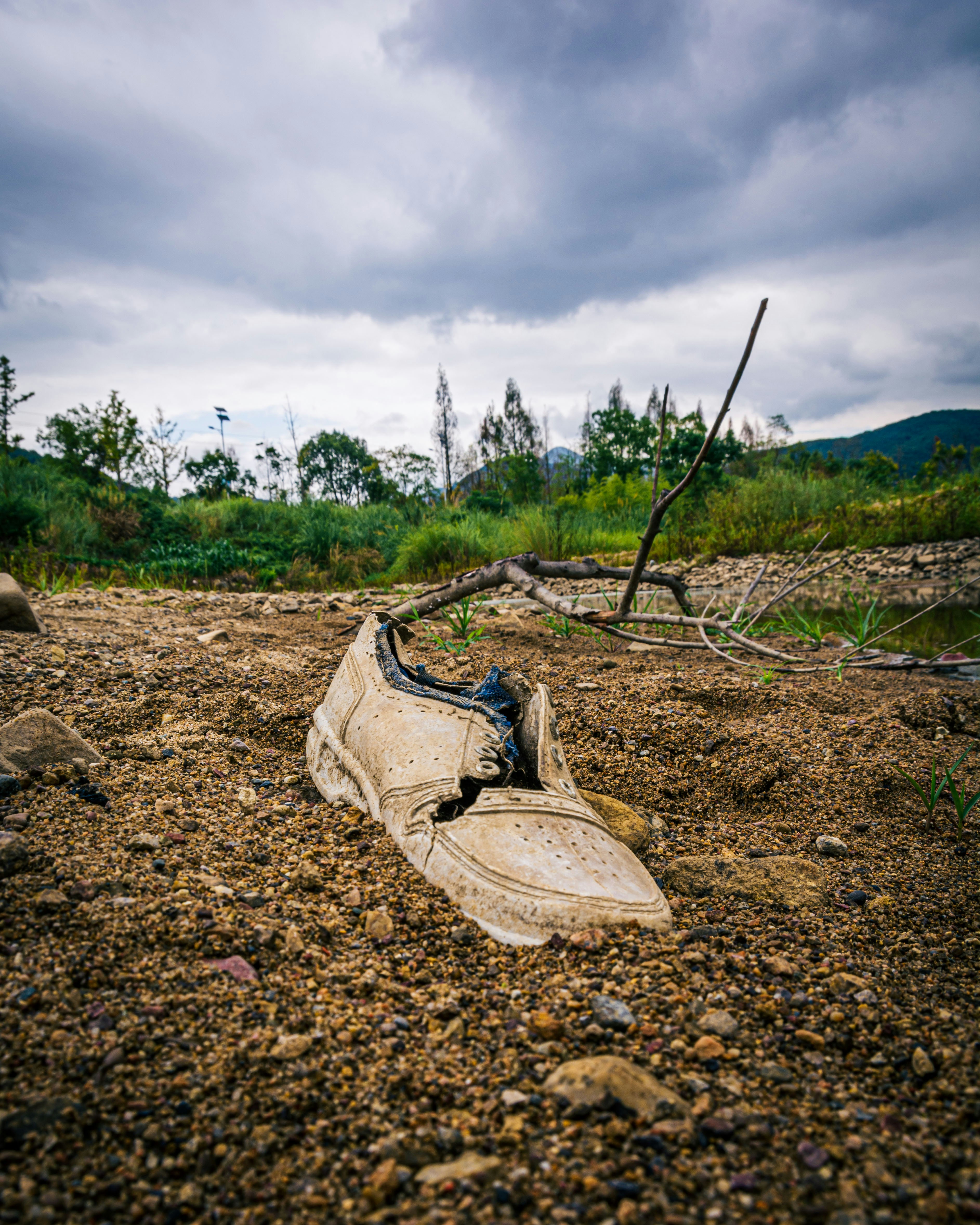Weathered Sneaker on a Gravel Riverside Beneath a Brooding Sky