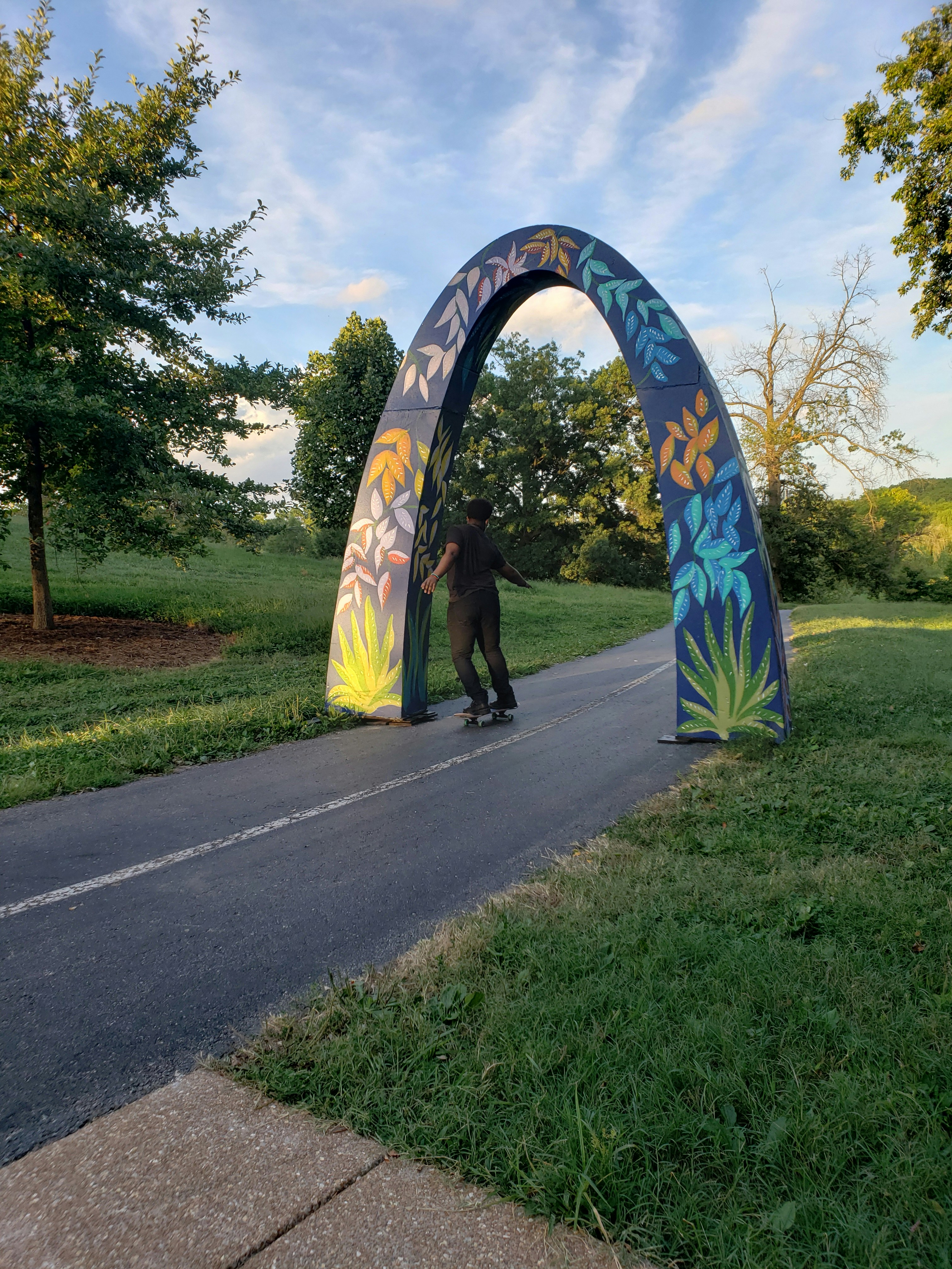 Skateboarder Glides Through a Painted Arch on a Quiet Park Path