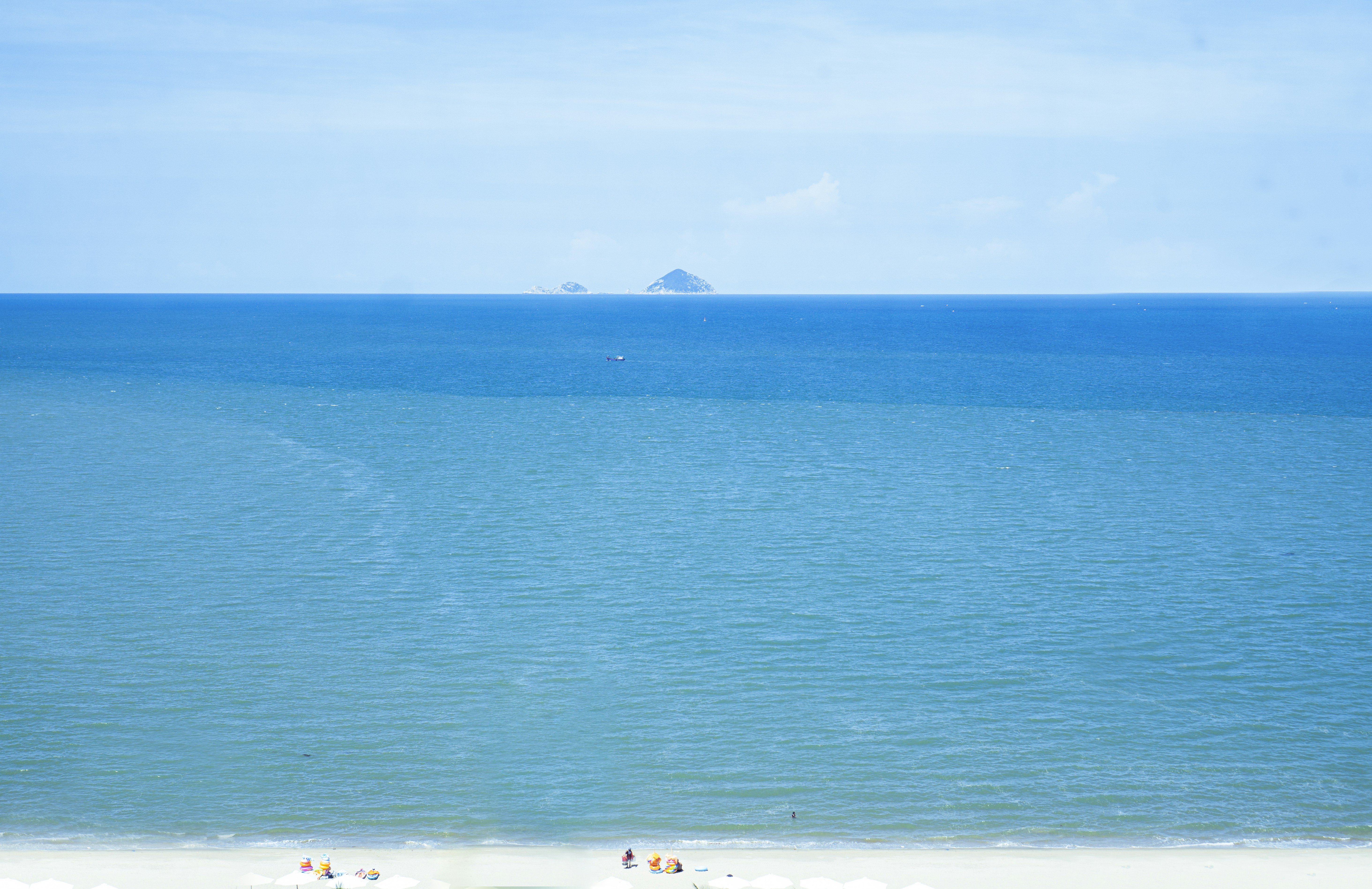 Expansive blue ocean meeting a clear sky with distant islands on the horizon.