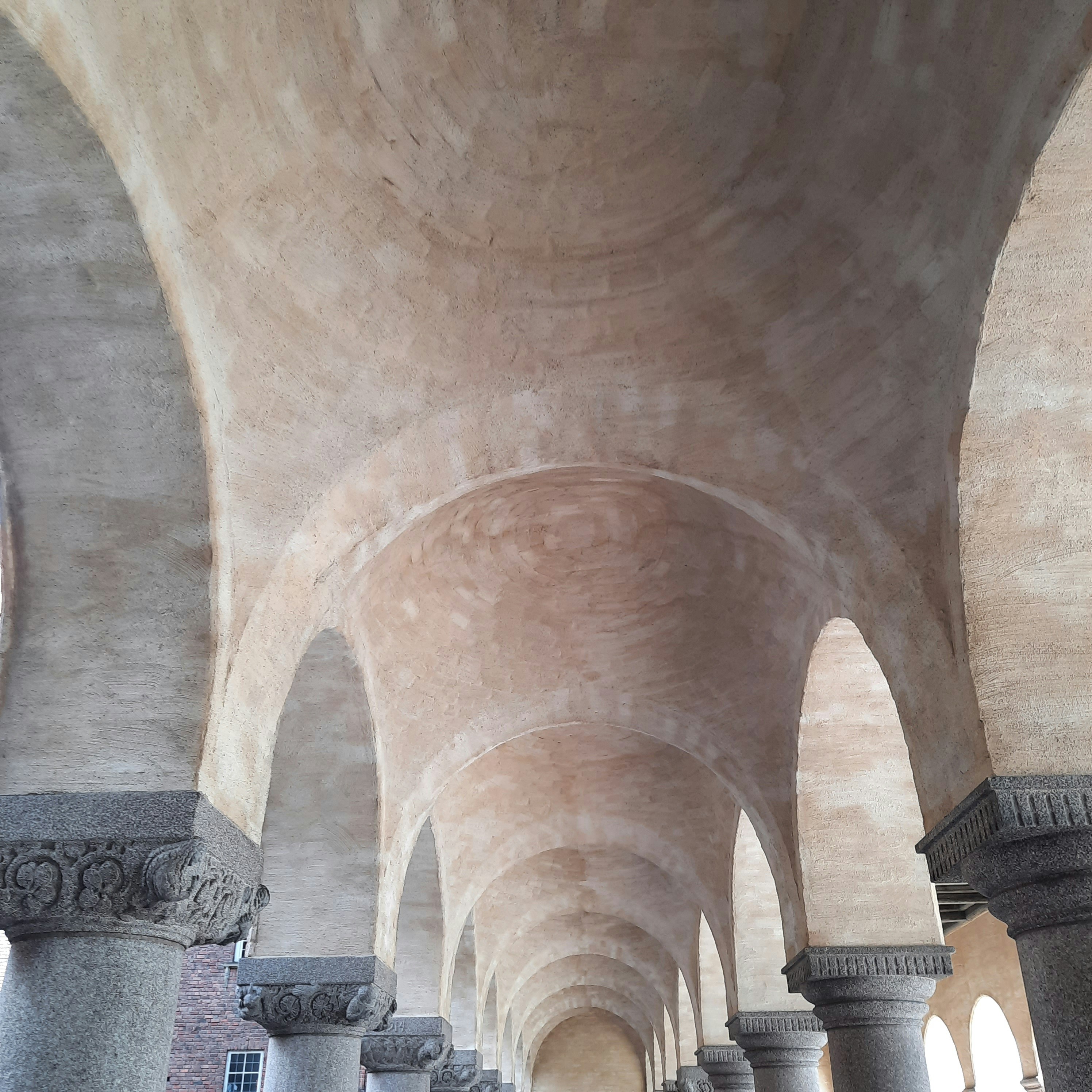 Elegant arches create a rhythmic pattern in an ancient corridor, showcasing intricate stonework and historical architecture.