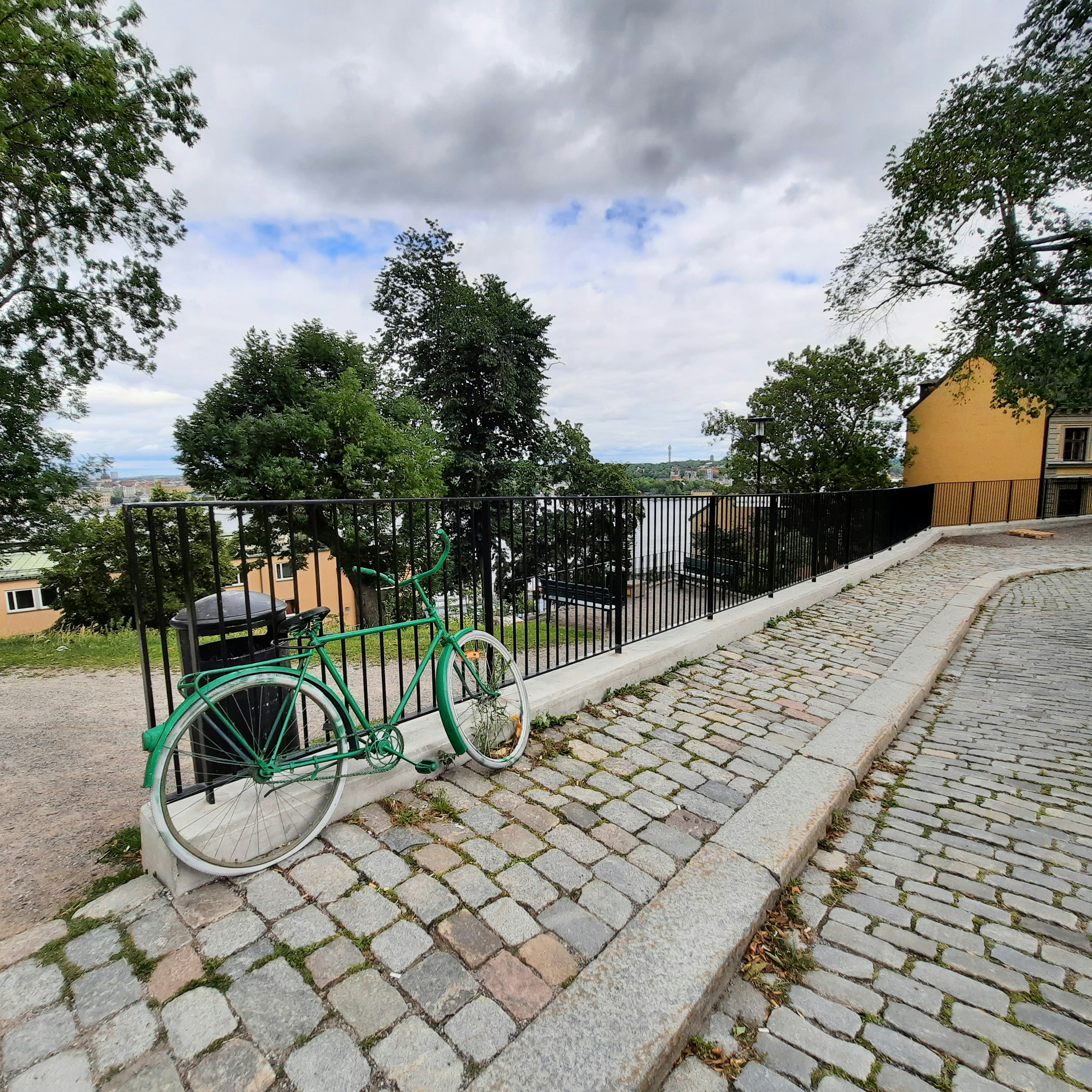A green retro bicycle leaning against a fence with a view of Stockholm harbour visible behind.