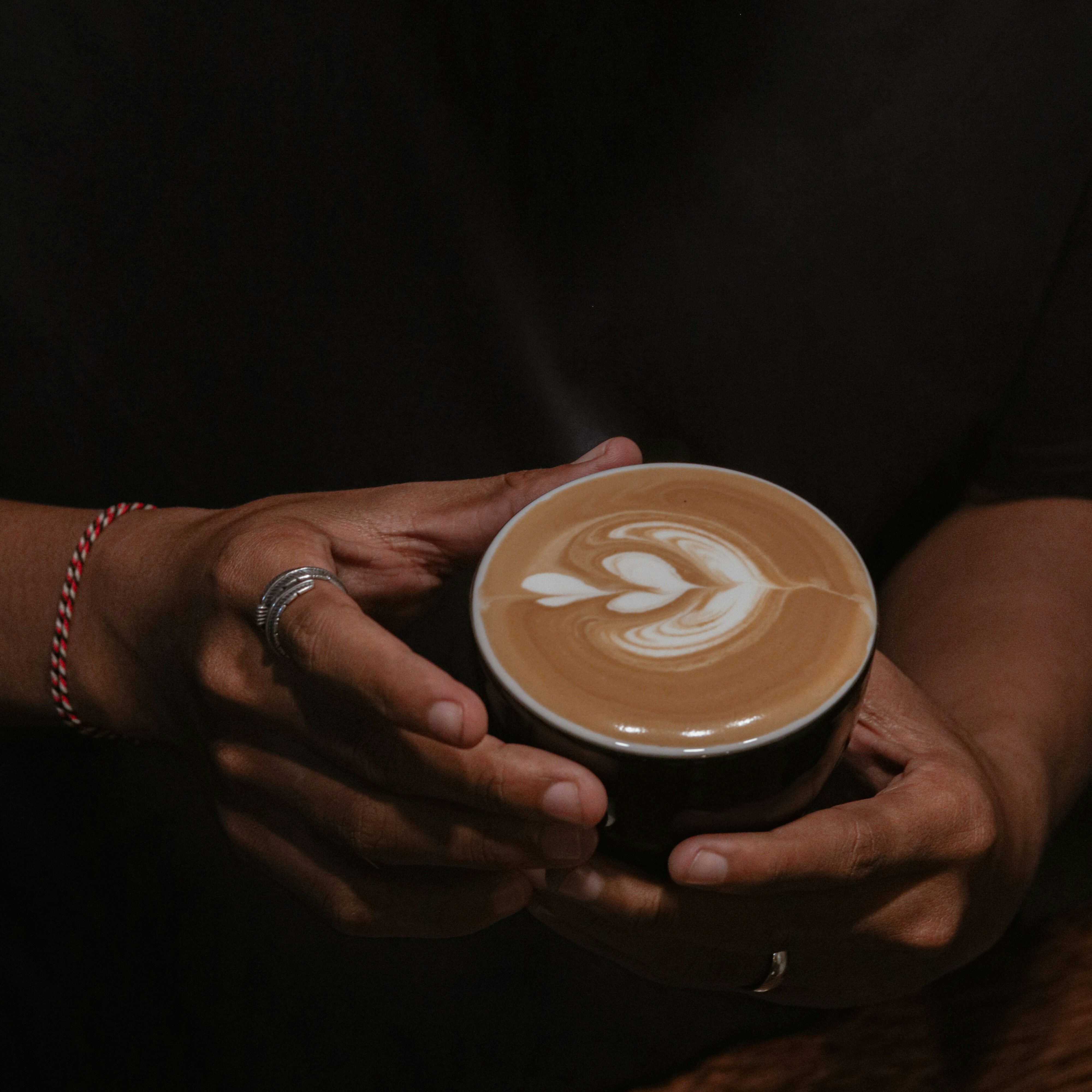 Moody Hands Cradle a Latte: Close-Up of Heart Latte Art in Dim Light