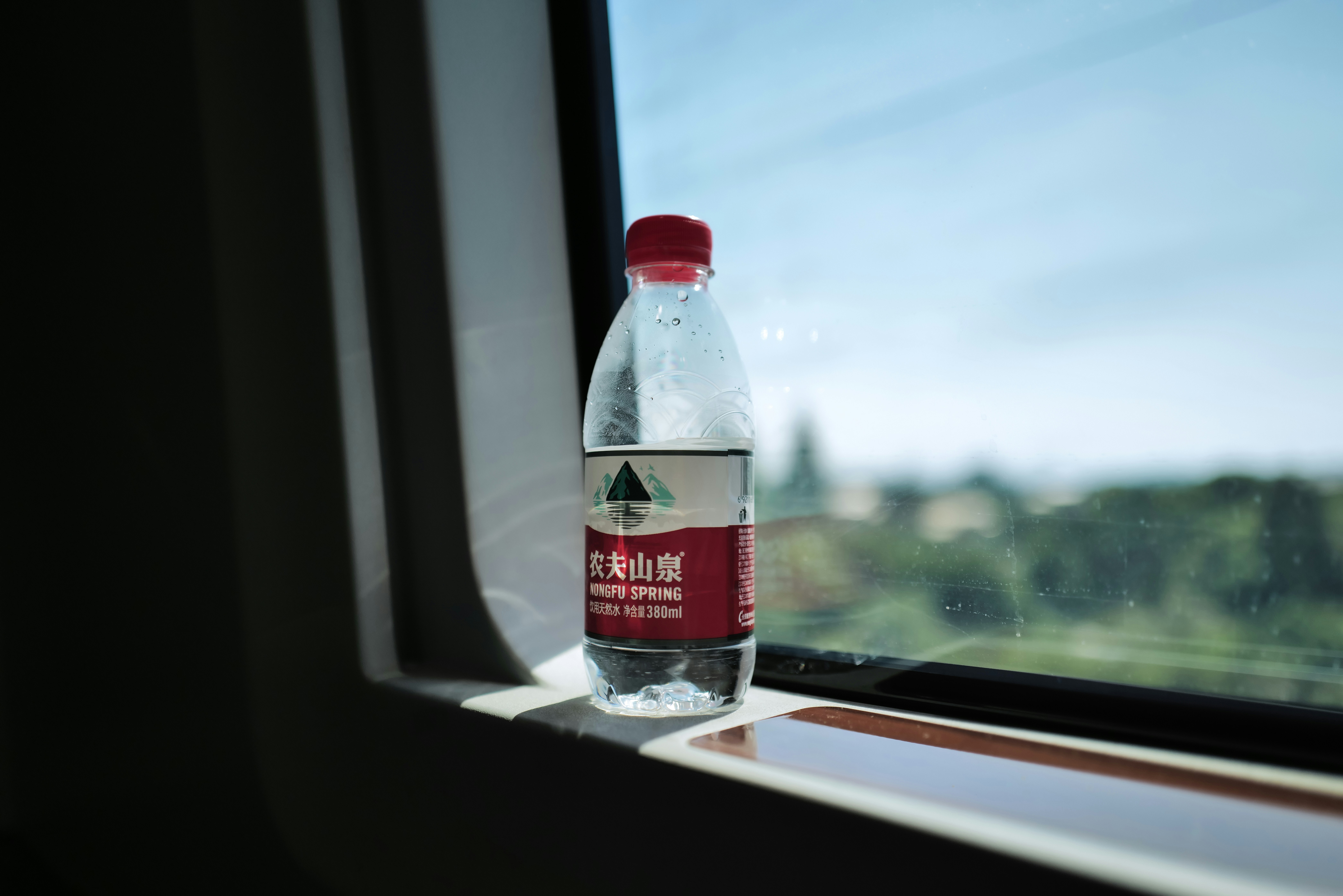 Sill Light: A Clear Water Bottle Anchoring a Quiet Train Window View