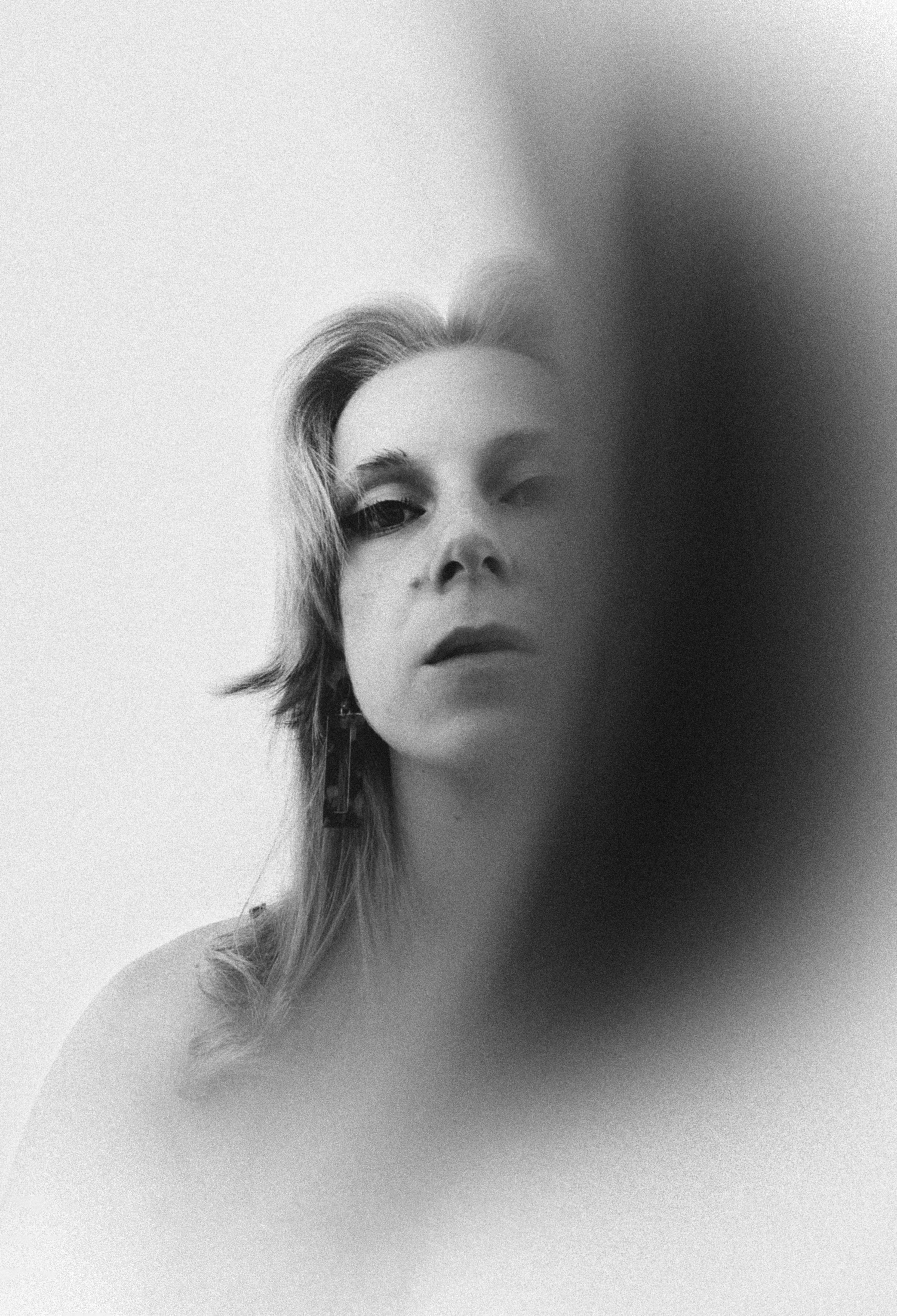 Black-and-white portrait photograph of a woman, with her face emerging from a soft haze that obscures the right side.