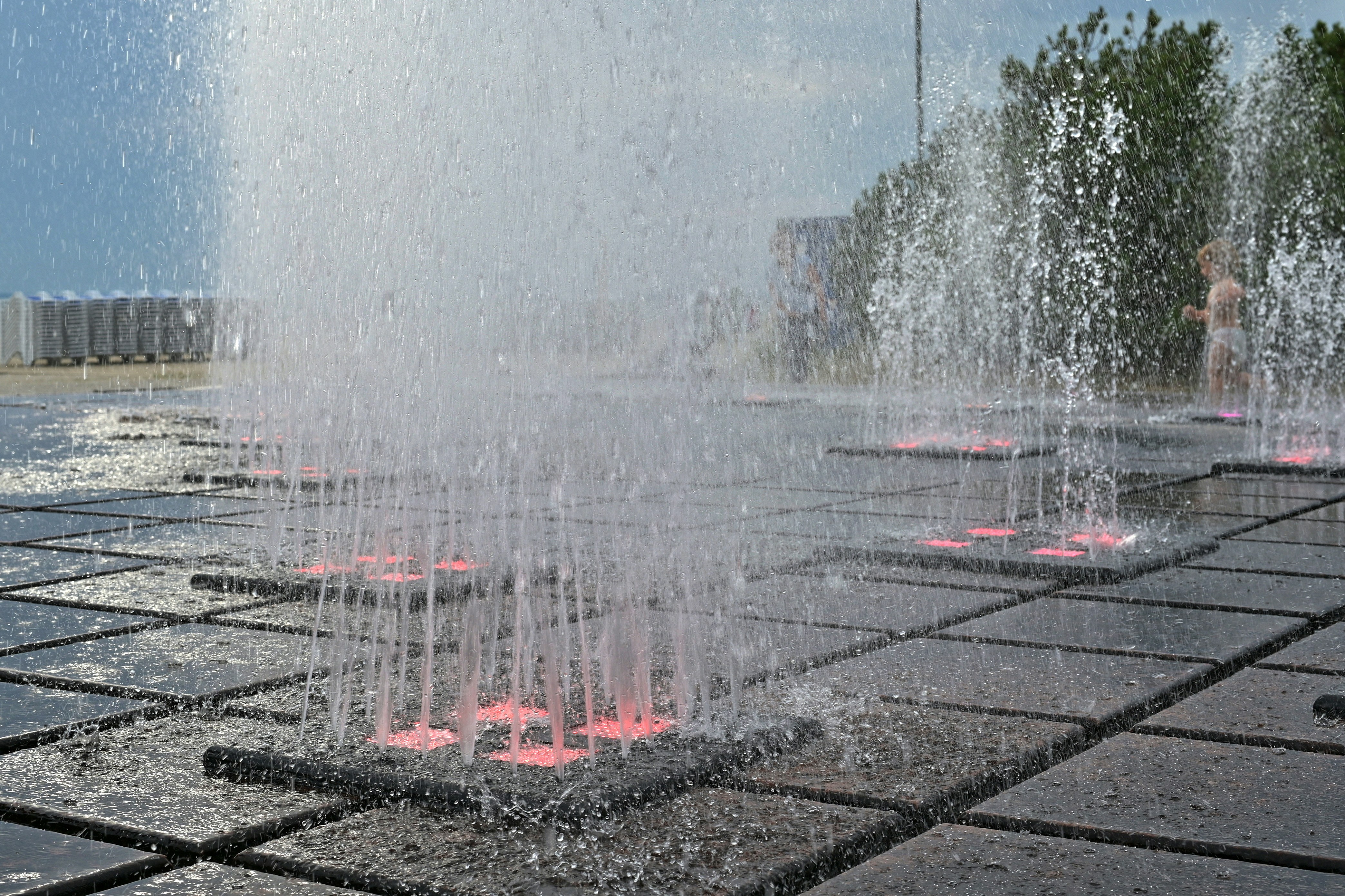 Neon-tinged jets bloom from a modular plaza fountain
