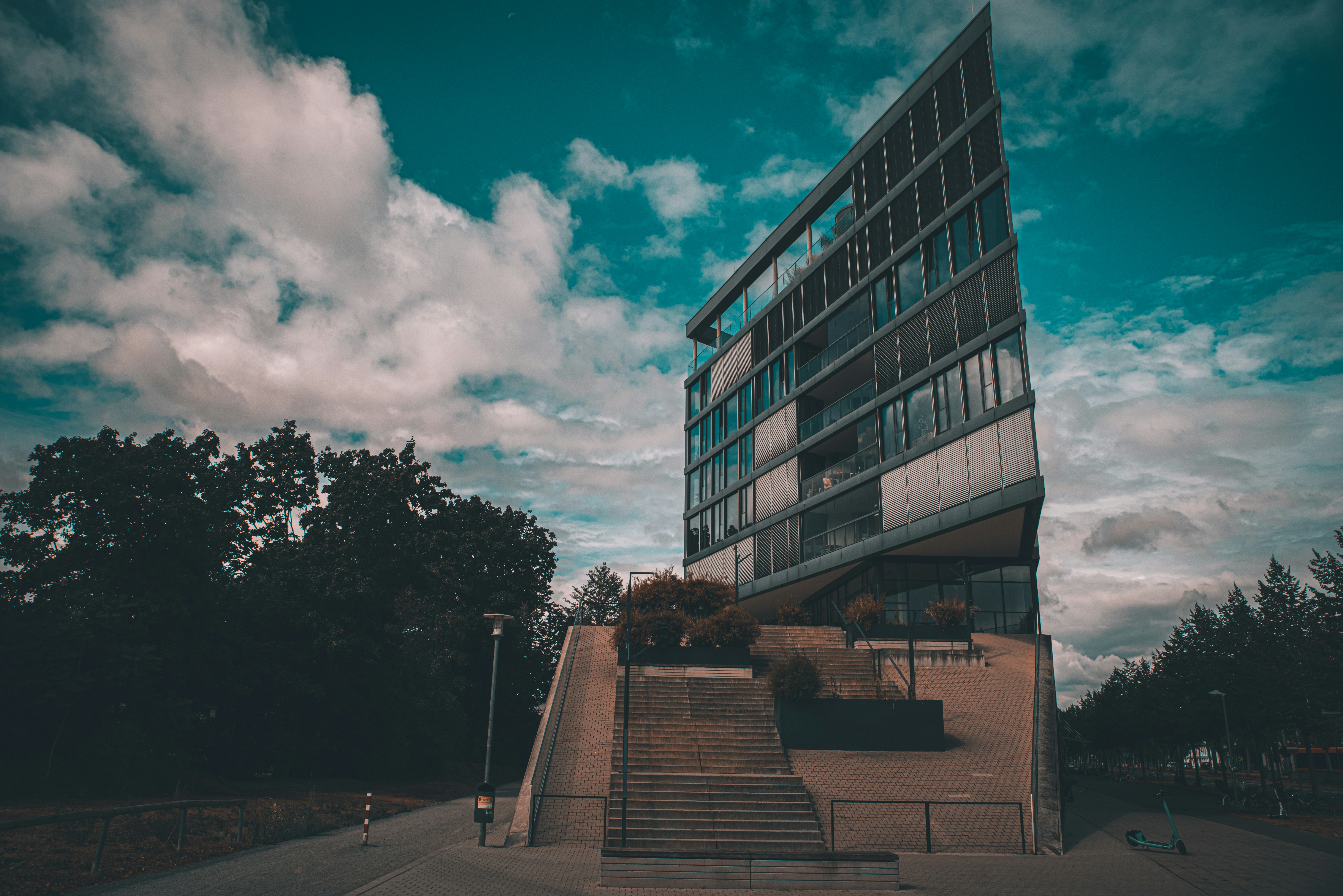 A striking modern building with an angular design, set against a dramatic sky, surrounded by lush greenery.