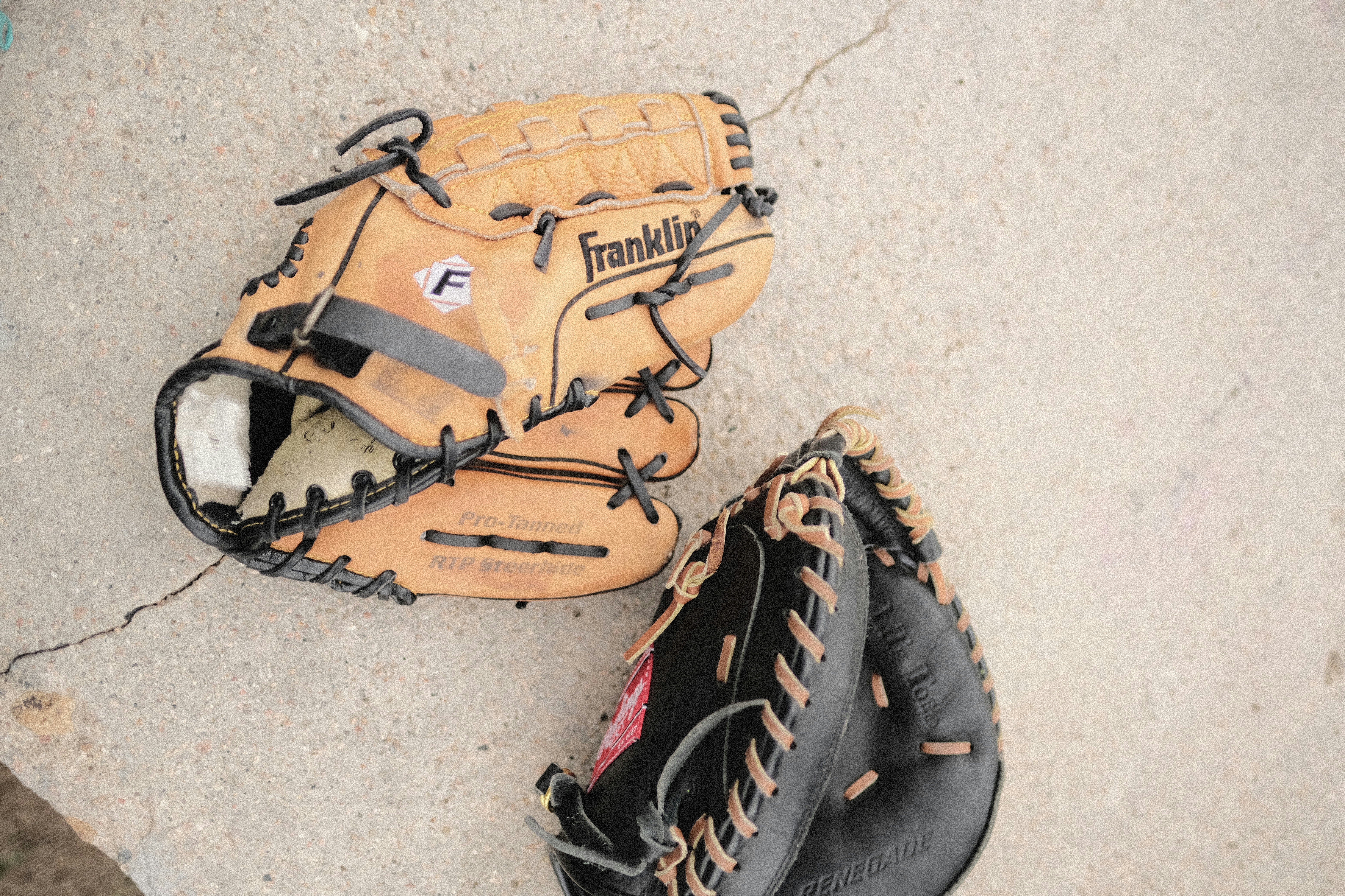 Two baseball gloves resting on a rough concrete surface.