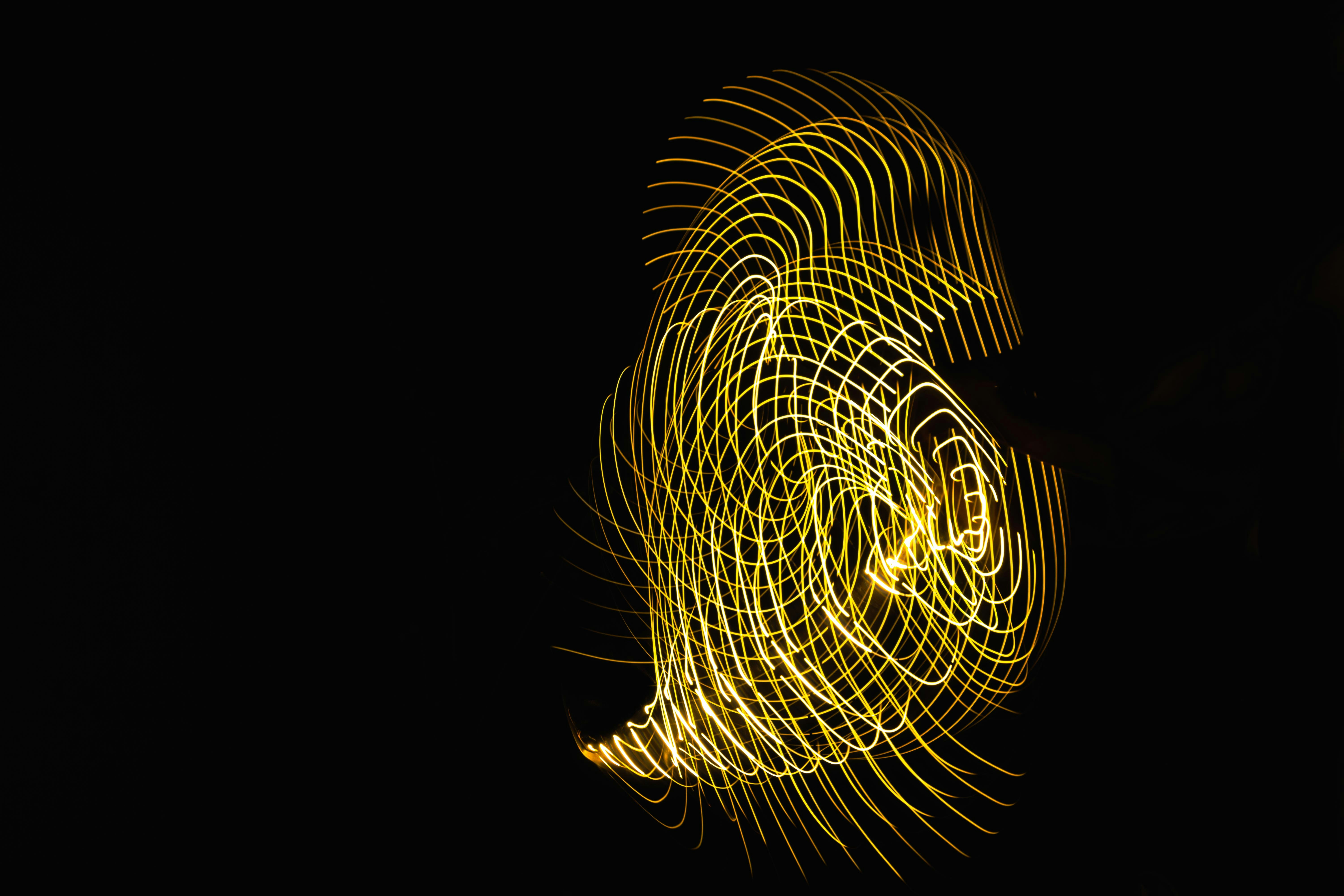 Swirling patterns of golden light create an abstract representation against a dark background, showcasing the fluidity of motion. The image captures the dynamic interplay of light and shadow.