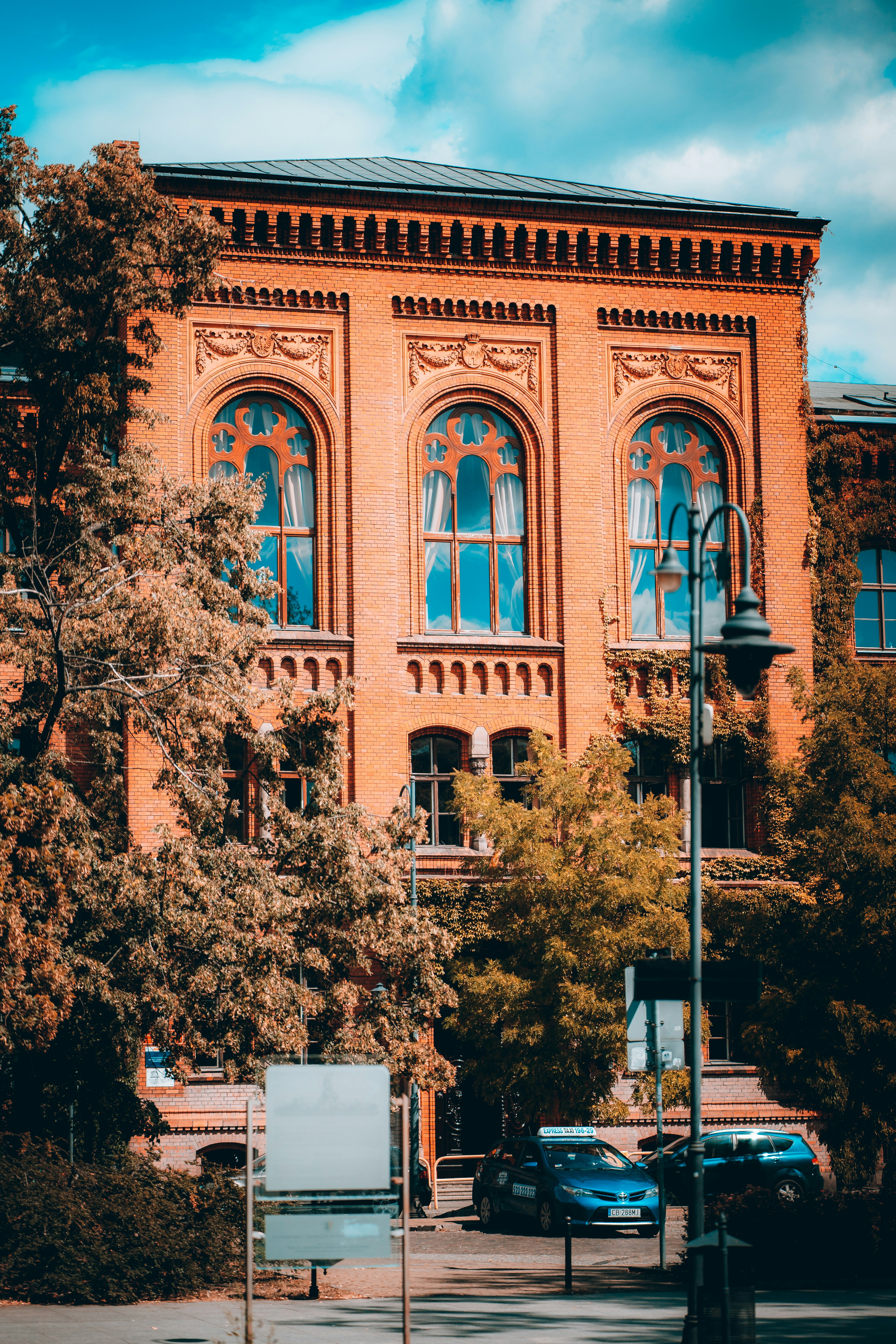 Historic brick building with arched windows surrounded by lush trees under a partly cloudy sky.