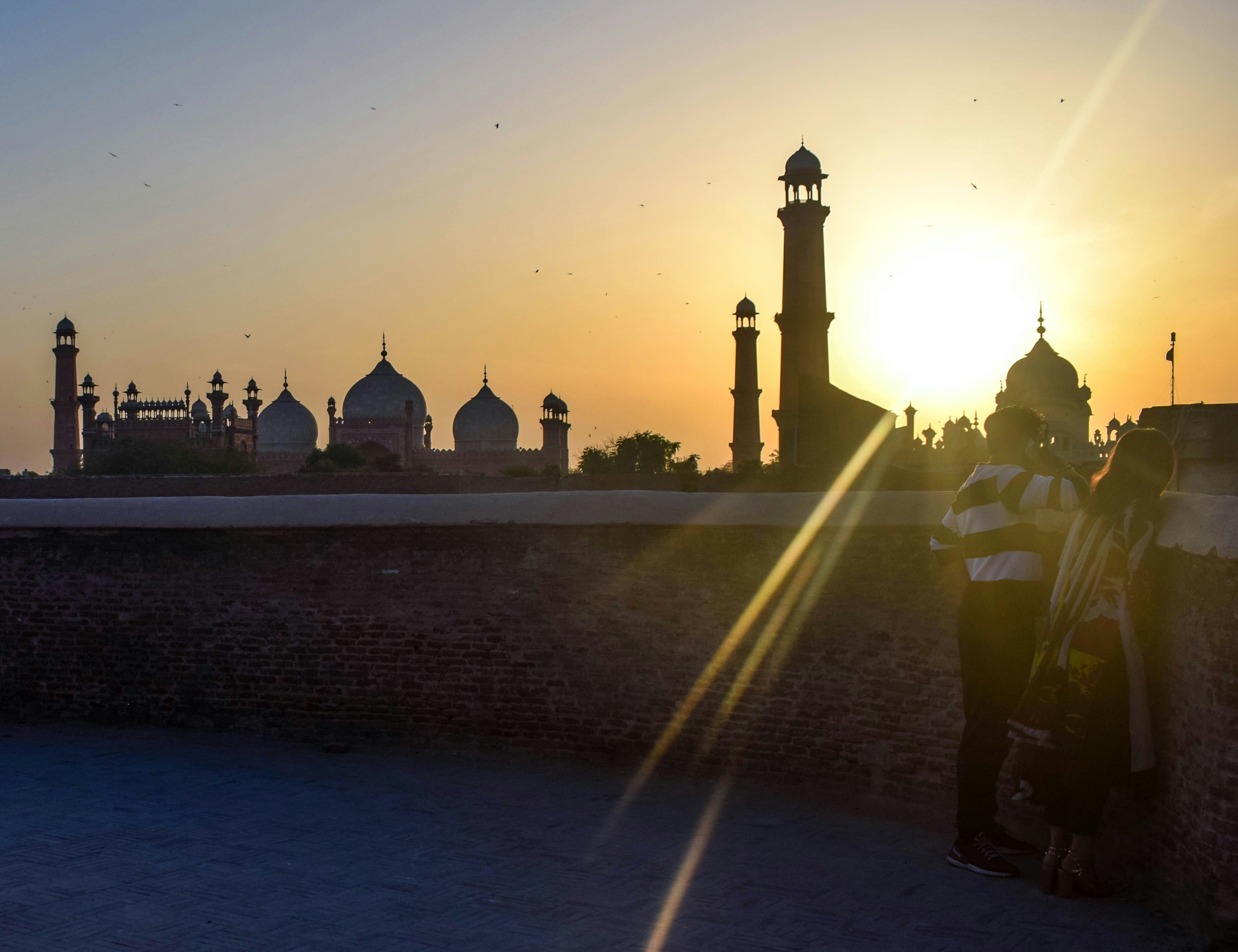Sunburst over a Mughal-inspired skyline as silhouettes linger on a riverside wall