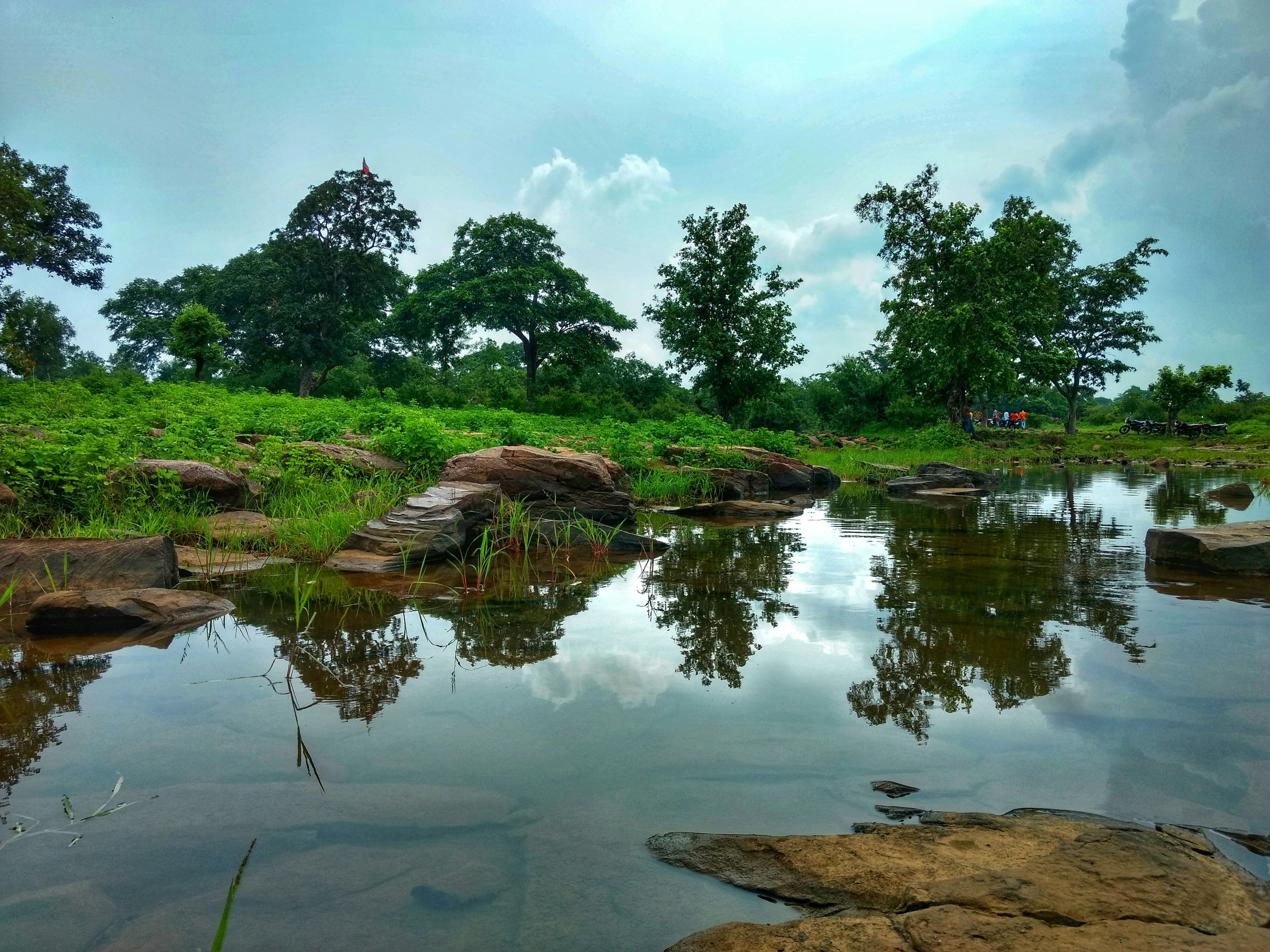 Tranquil riverscape with stone ledges and a tree-lined bank mirrored in calm water. This landscape photograph captures the quiet interplay of rock, water, and reflected sky.