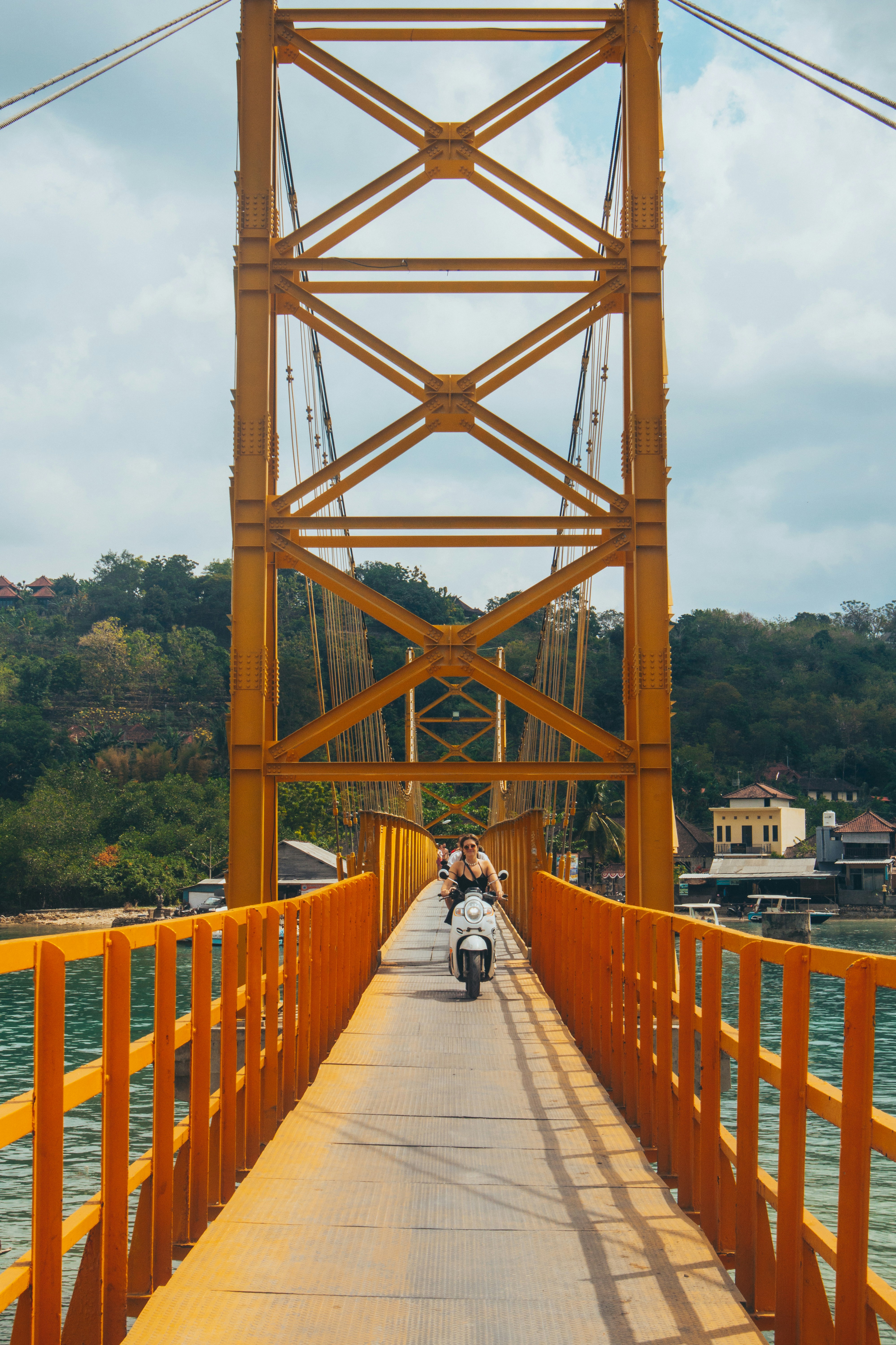 Center-Frame Scooter Crossing on a Golden Suspension Bridge