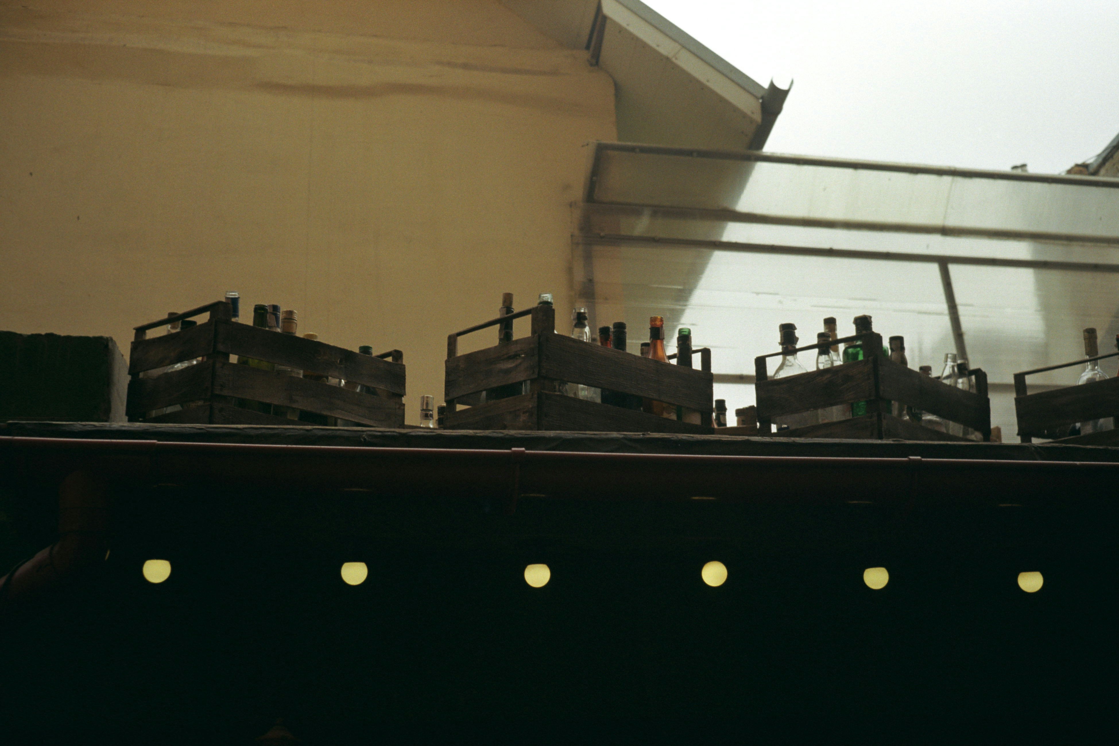 Wooden crates filled with bottles sit atop a rooftop, framed by a modern architectural backdrop. The scene captures a blend of urban life and casual relaxation.