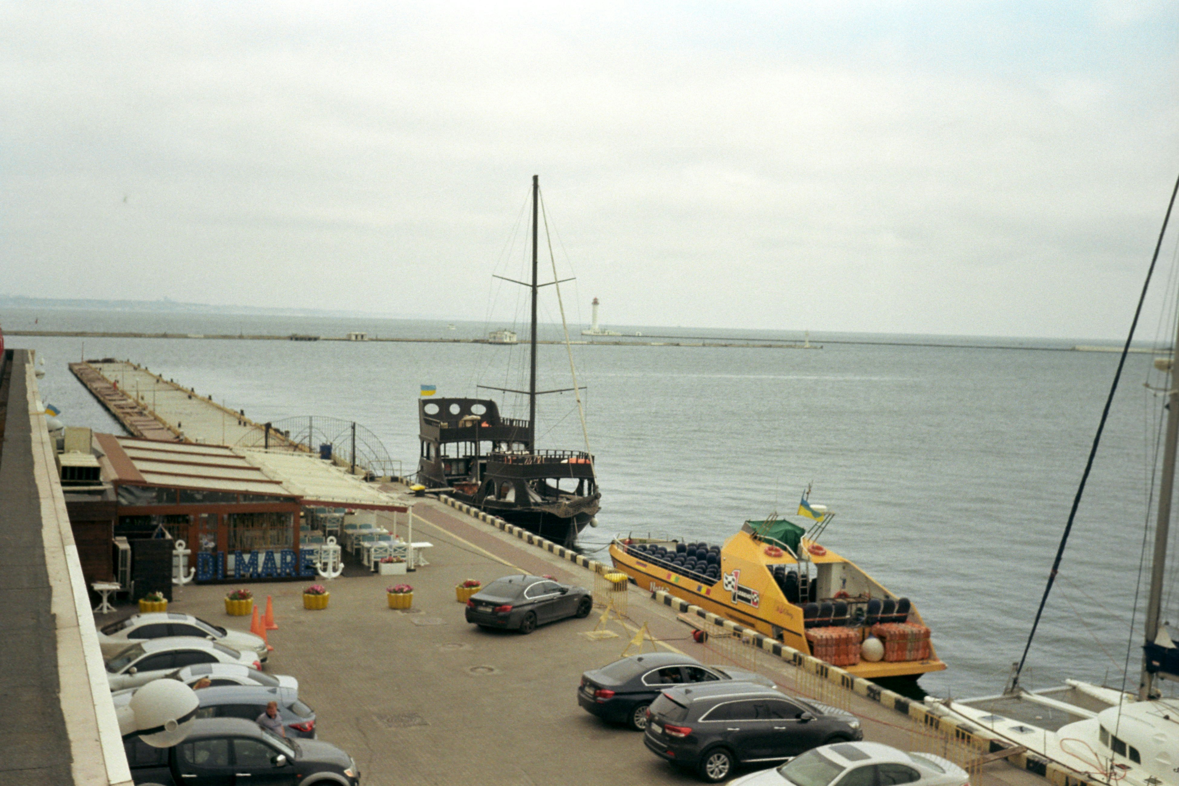 Harbor pier with parked cars, a distant mast, and a yellow workboat by the quay.