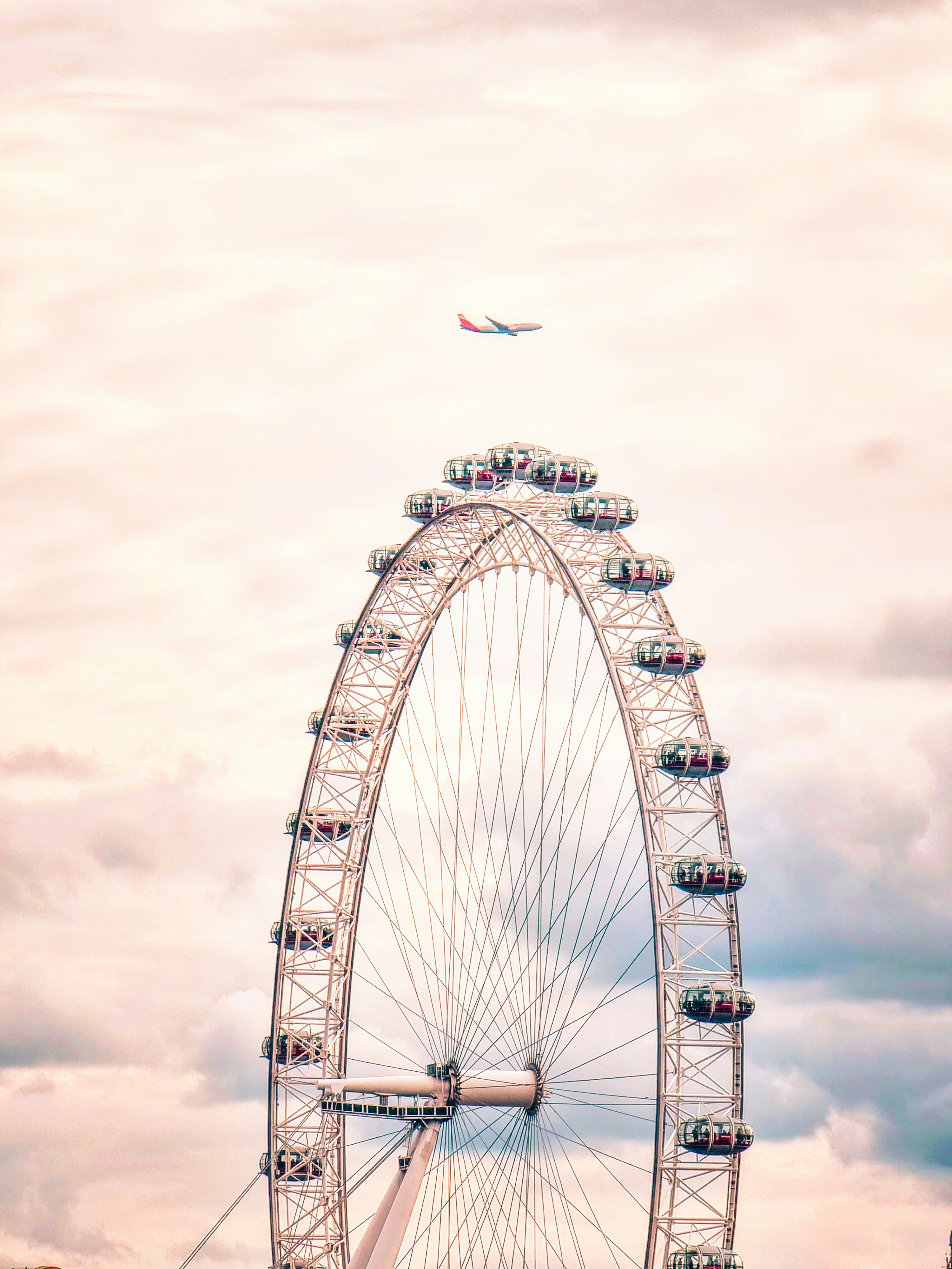 Ferris wheel framed against a pastel sky with a plane soaring above, highlighting the intersection of leisure and travel.