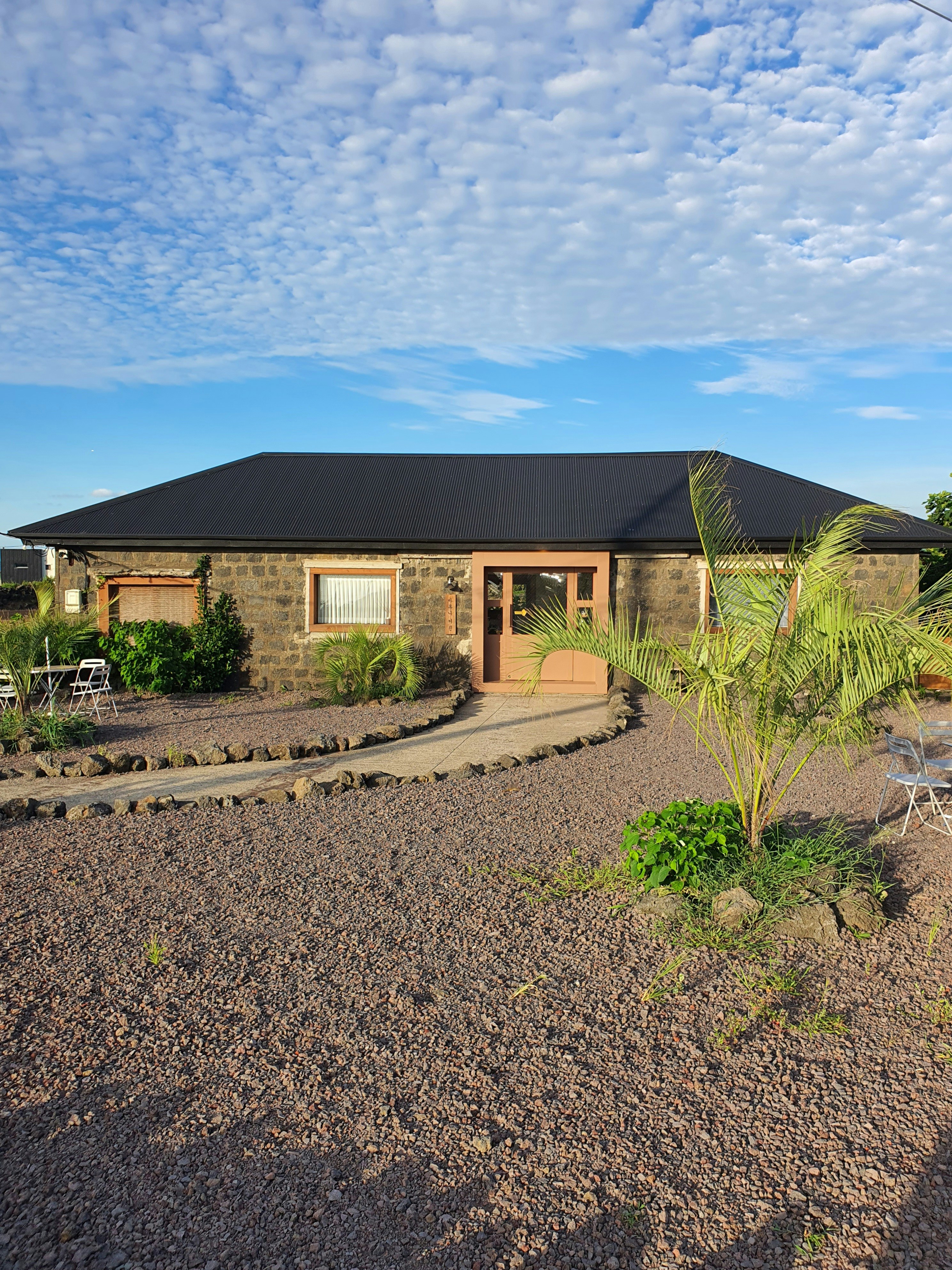 Charming stone house surrounded by lush greenery and gravel pathways, under a vibrant sky.