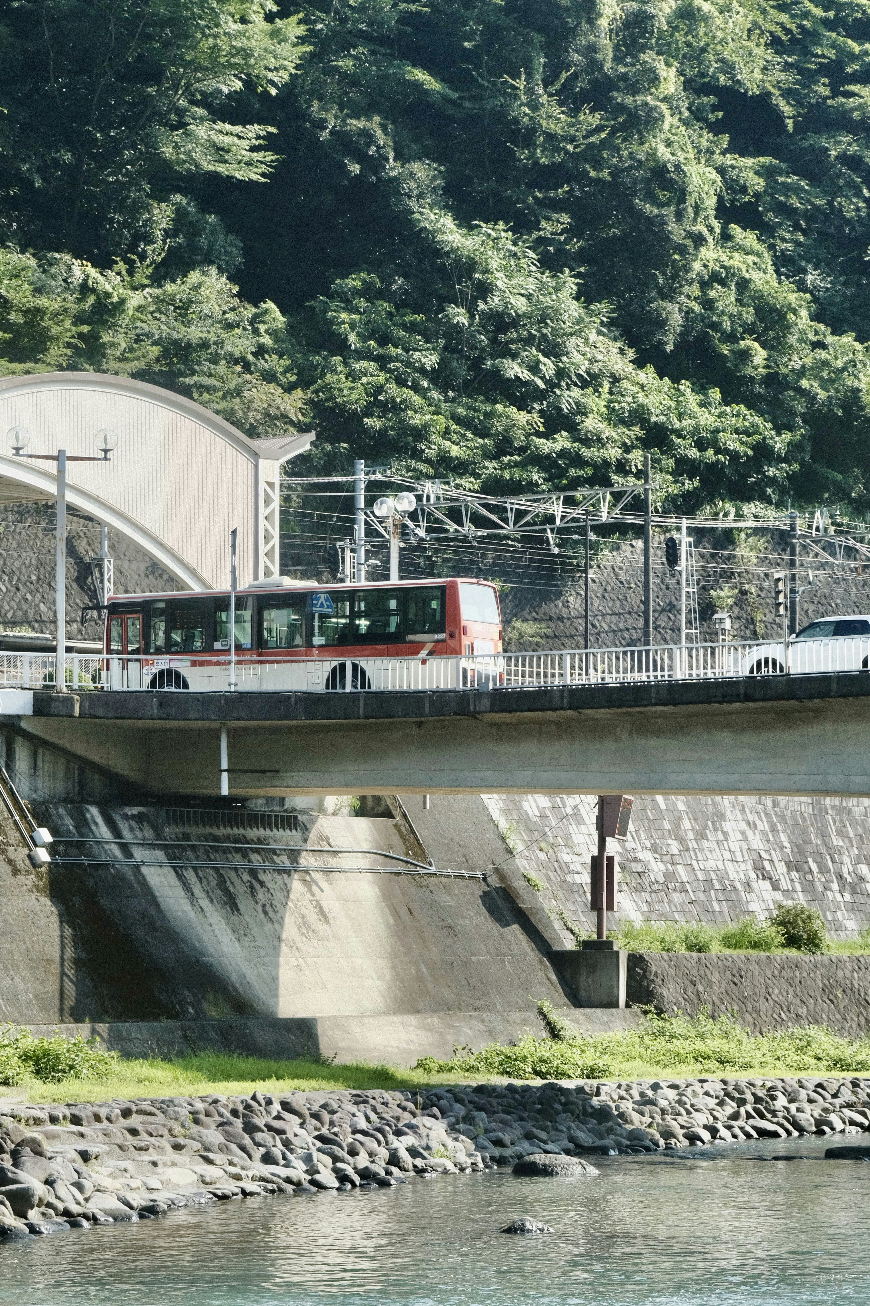 Red-White Transit Bus Crossing a River Bridge Beneath Forested Hills
