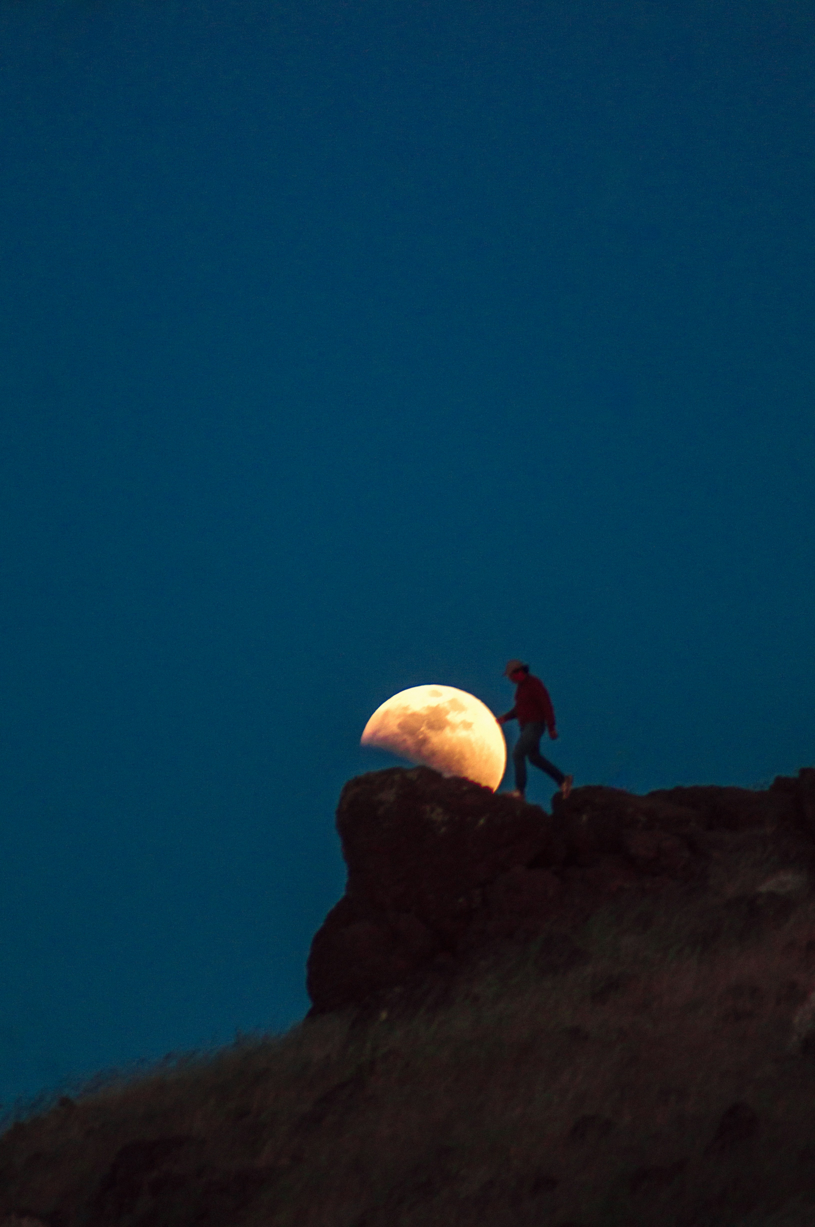 Silhouette of a climber scaling a rocky outcrop beneath a large, glowing moon in a twilight sky.