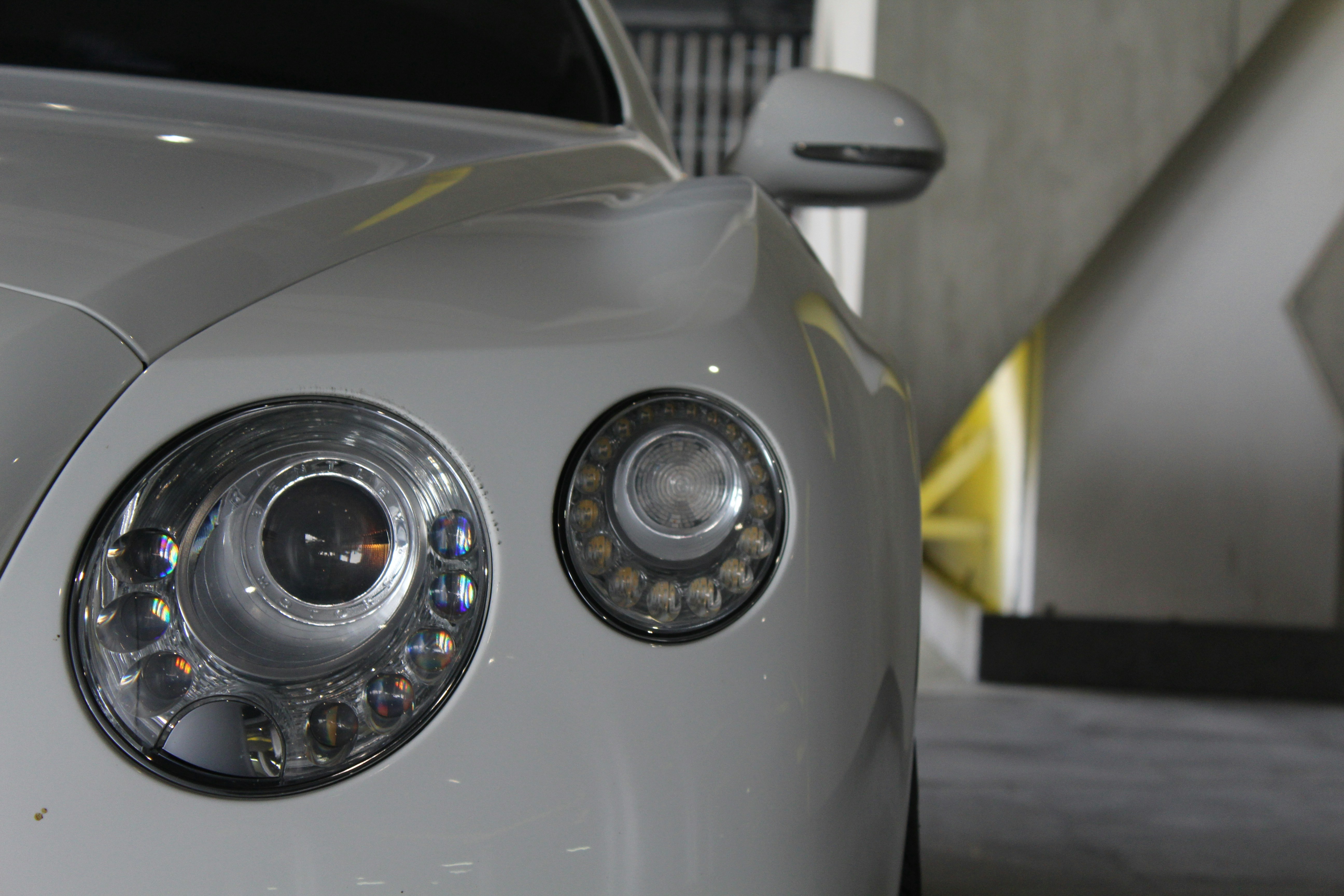 Close-up of a silver sports car headlight gleam in a shadowed parking area