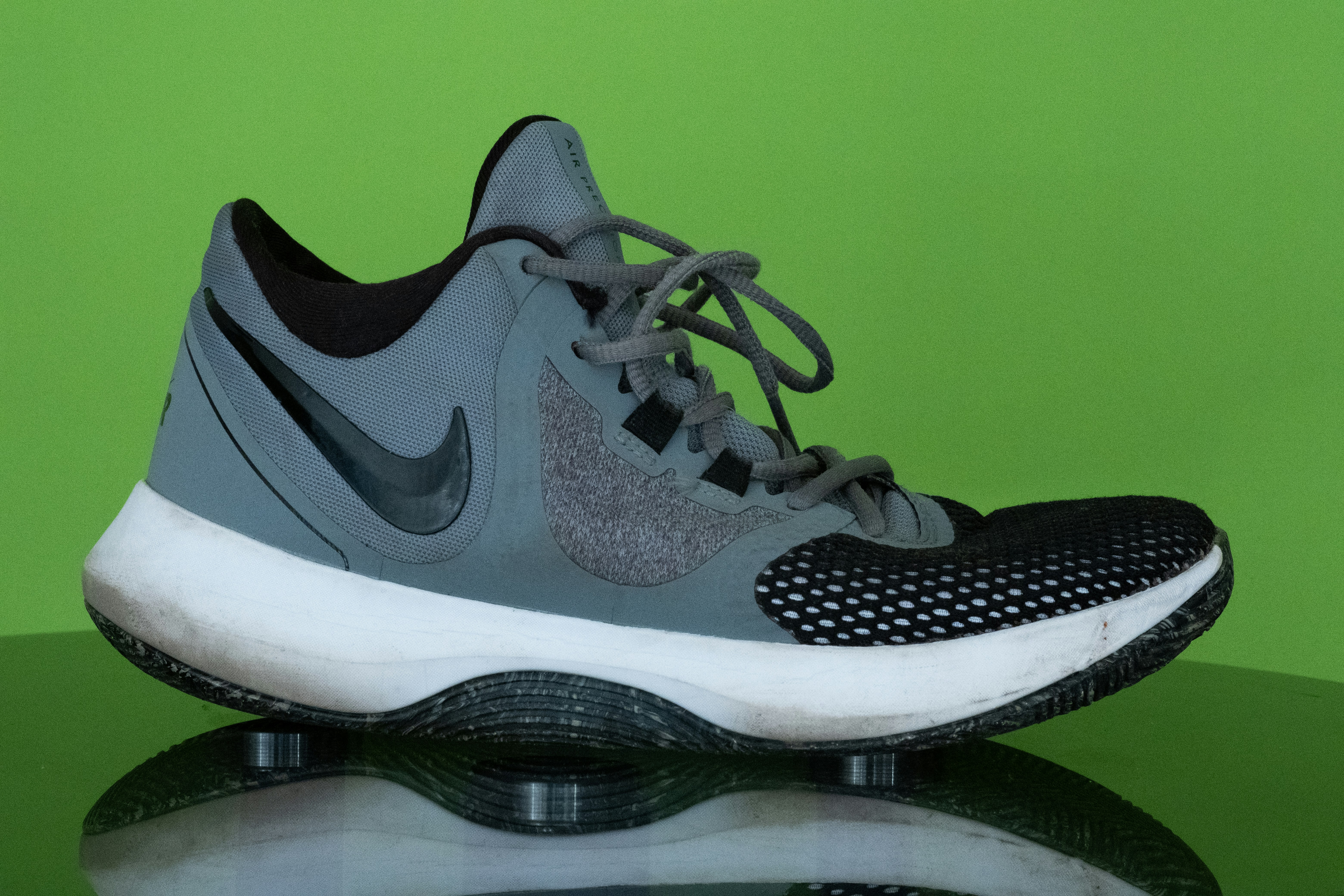 Lime-lit Sprint: A gray Nike running shoe resting on a glossy pedestal.