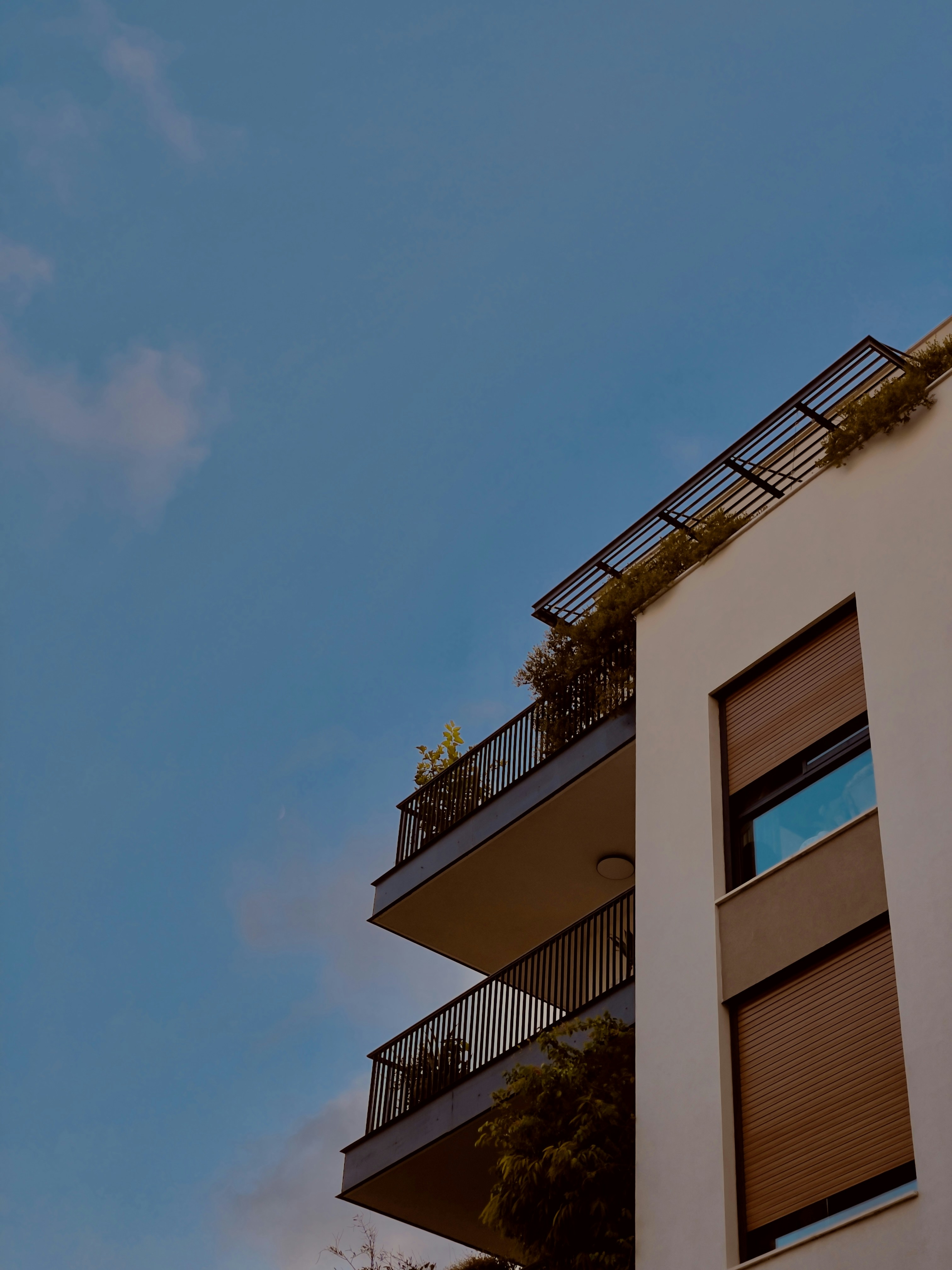 Contemporary building corner featuring balconies adorned with greenery against a blue sky.