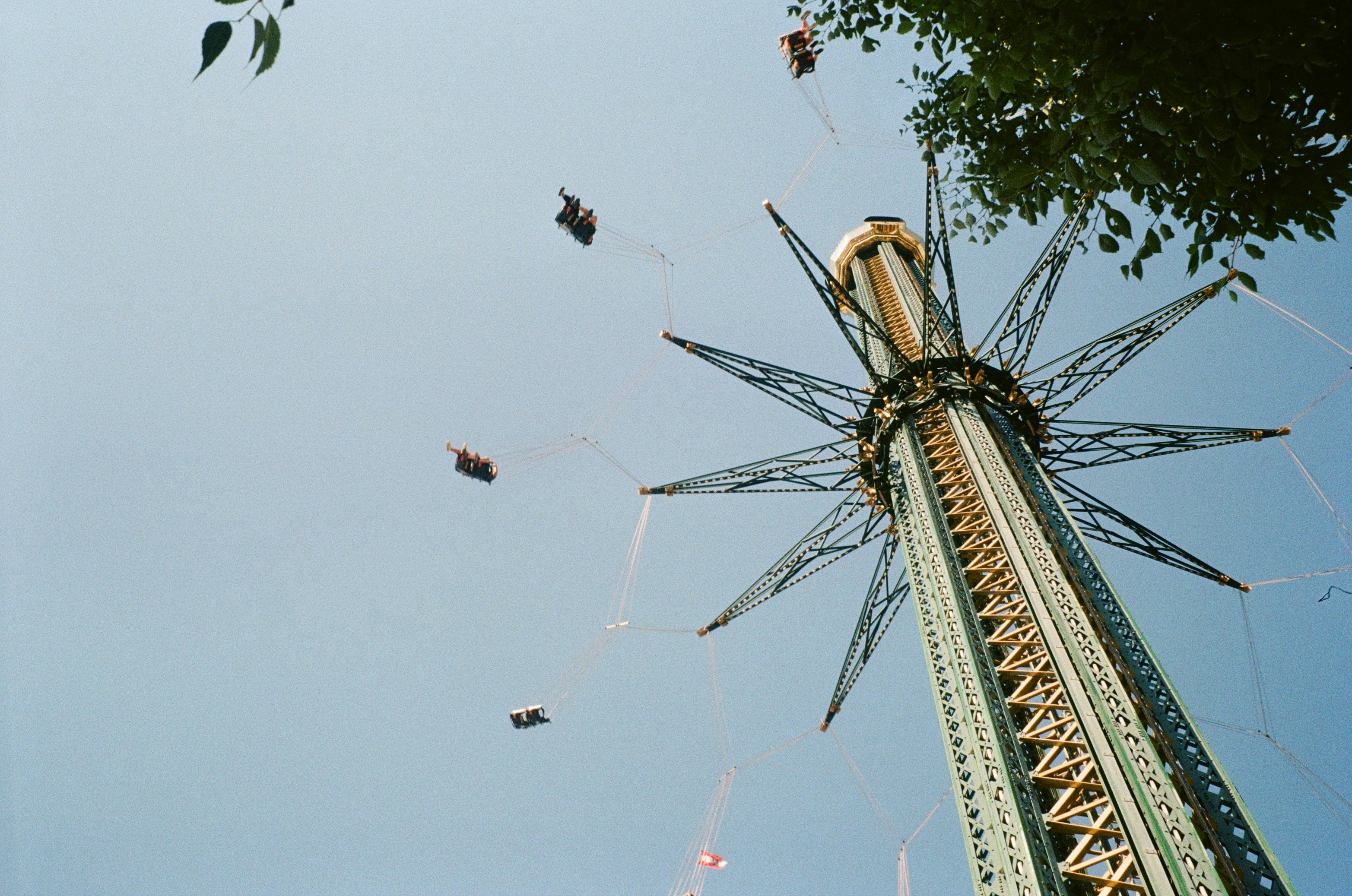 A towering amusement park ride spins joyfully against a clear blue sky, with riders suspended in the air. The structure's intricate design showcases engineering marvels.