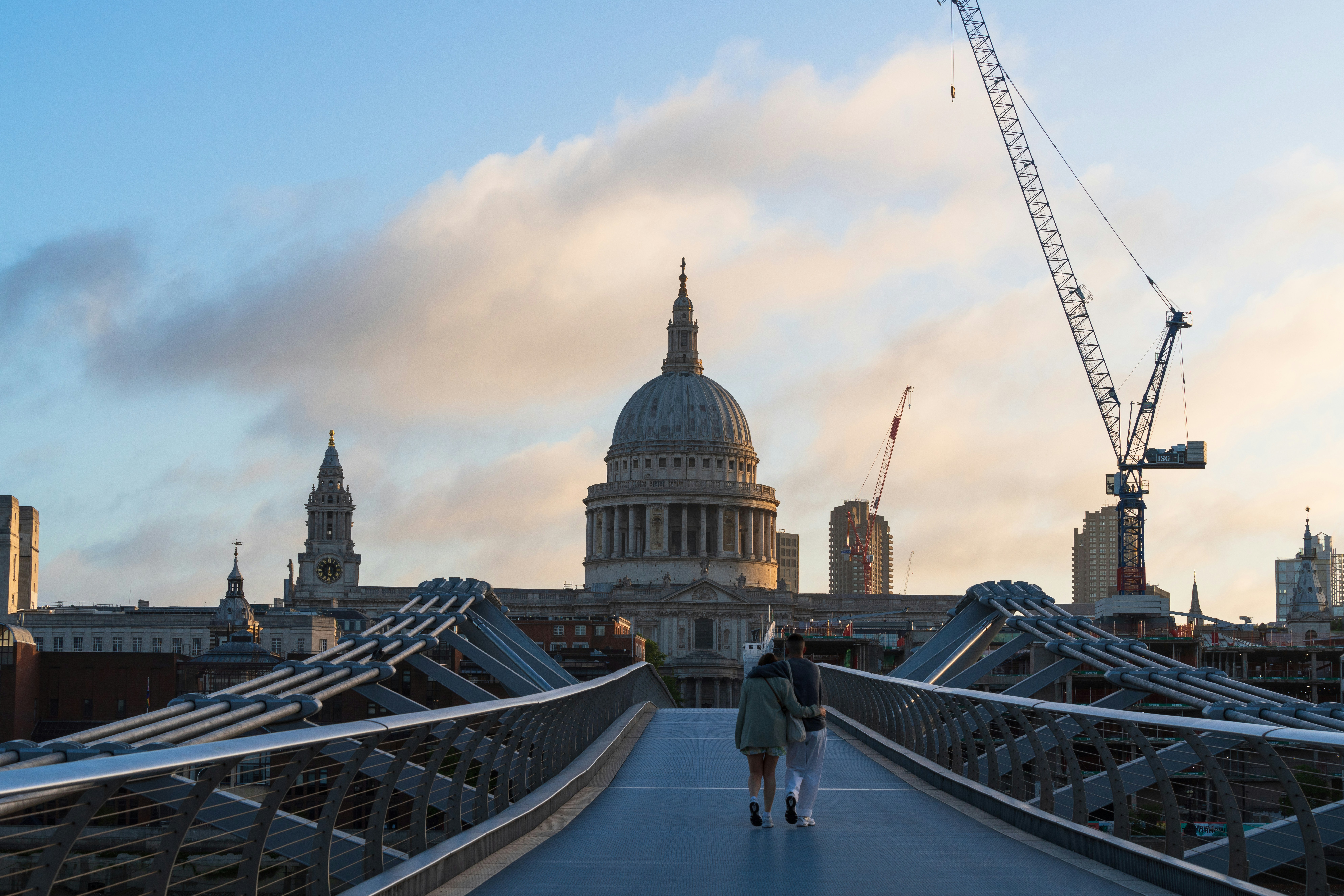 Couple walking on the Millennium Bridge with St. Paul's Cathedral in the background, framed by a construction crane. 