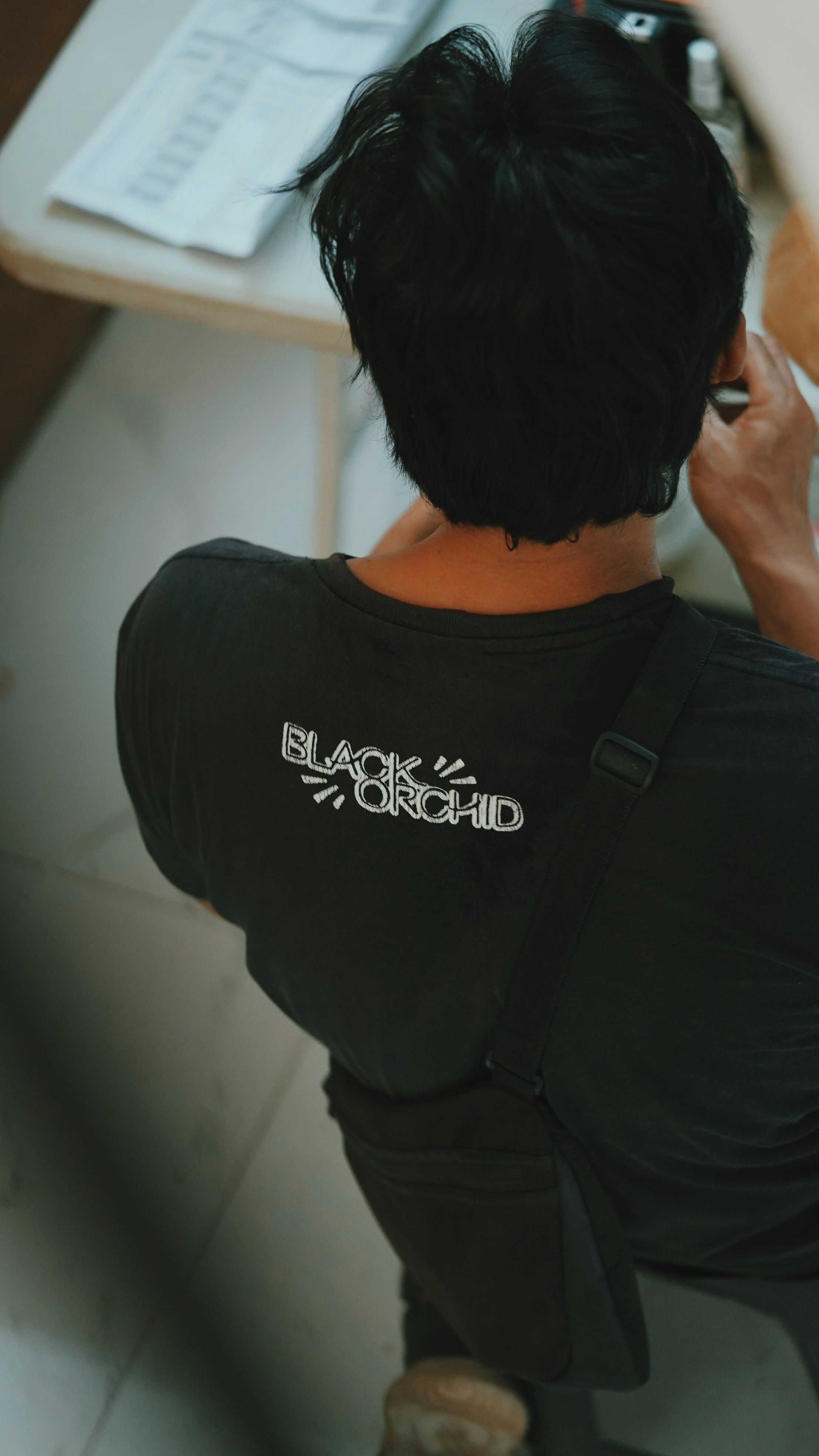 Individual focused on a task while wearing a shirt with 'BLACK ORCHID' branding, surrounded by tools and materials.