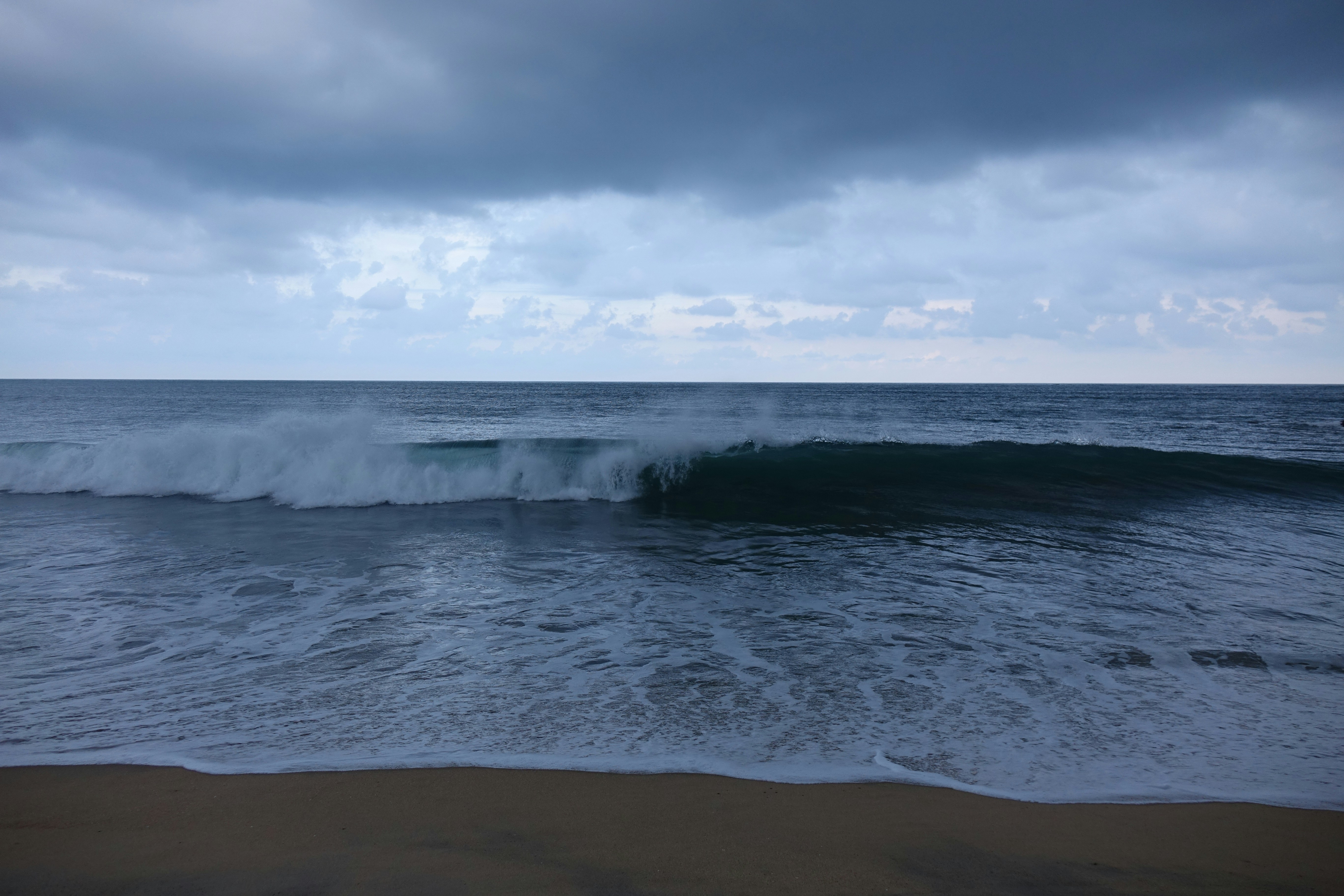 Rolling waves cresting under a moody sky, capturing the essence of a tranquil shoreline. The blend of sea and sand evokes a sense of calm.