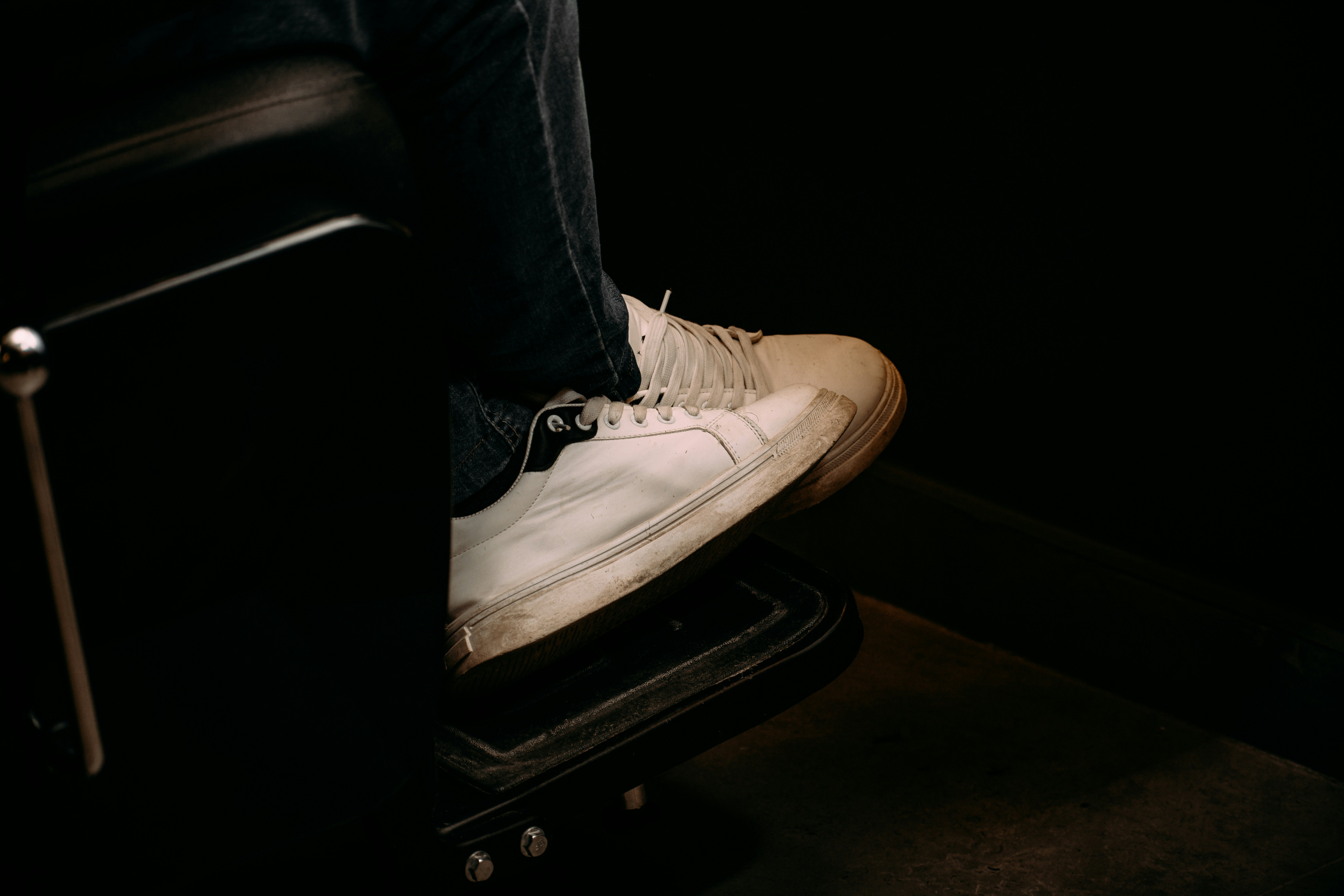 A close-up of a white sneaker resting on a footrest, set against a dark background, evoking a sense of casual comfort.