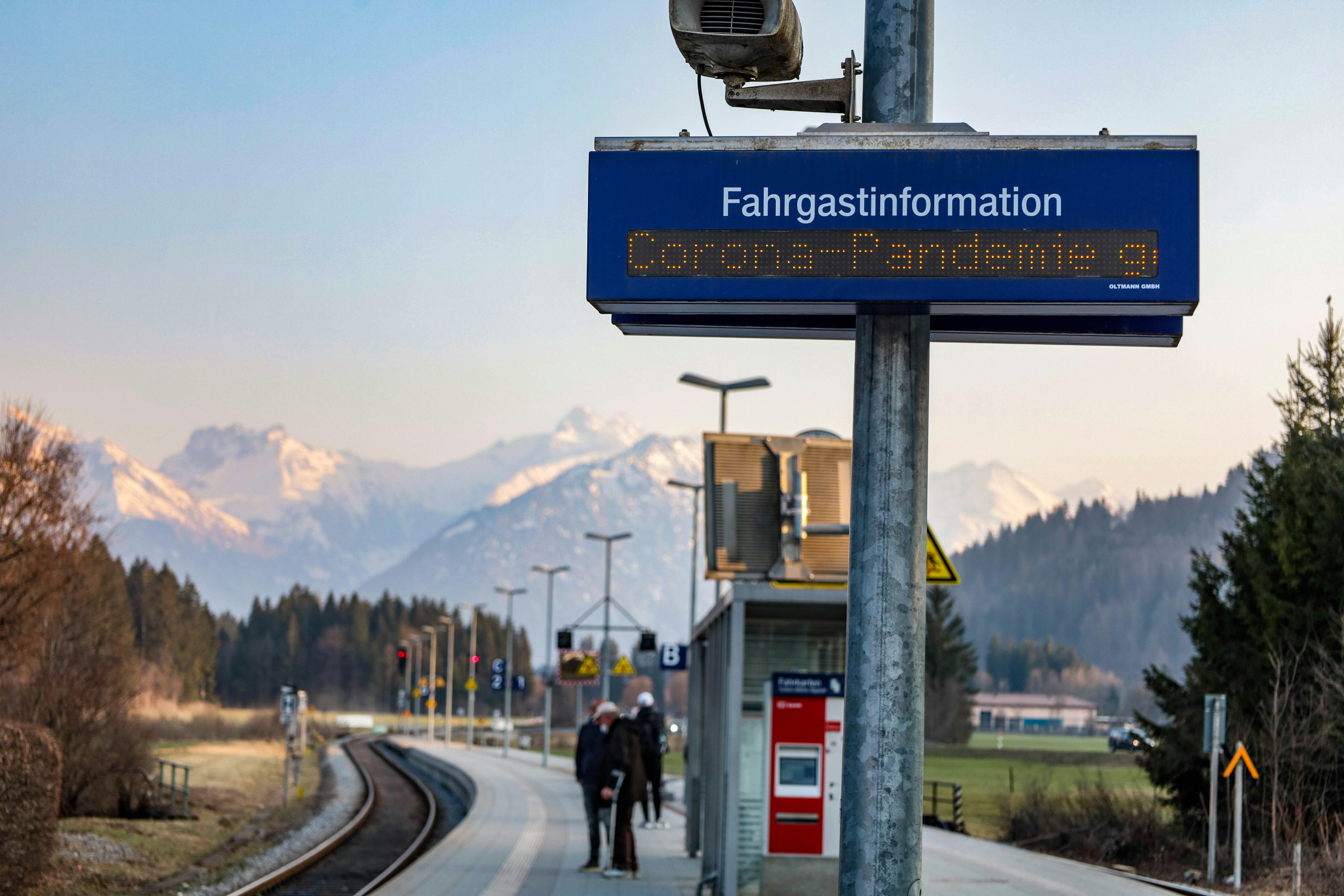 Alpine Rail Stop at Dusk: LED Information Sign Framed by Snow-Capped Peaks