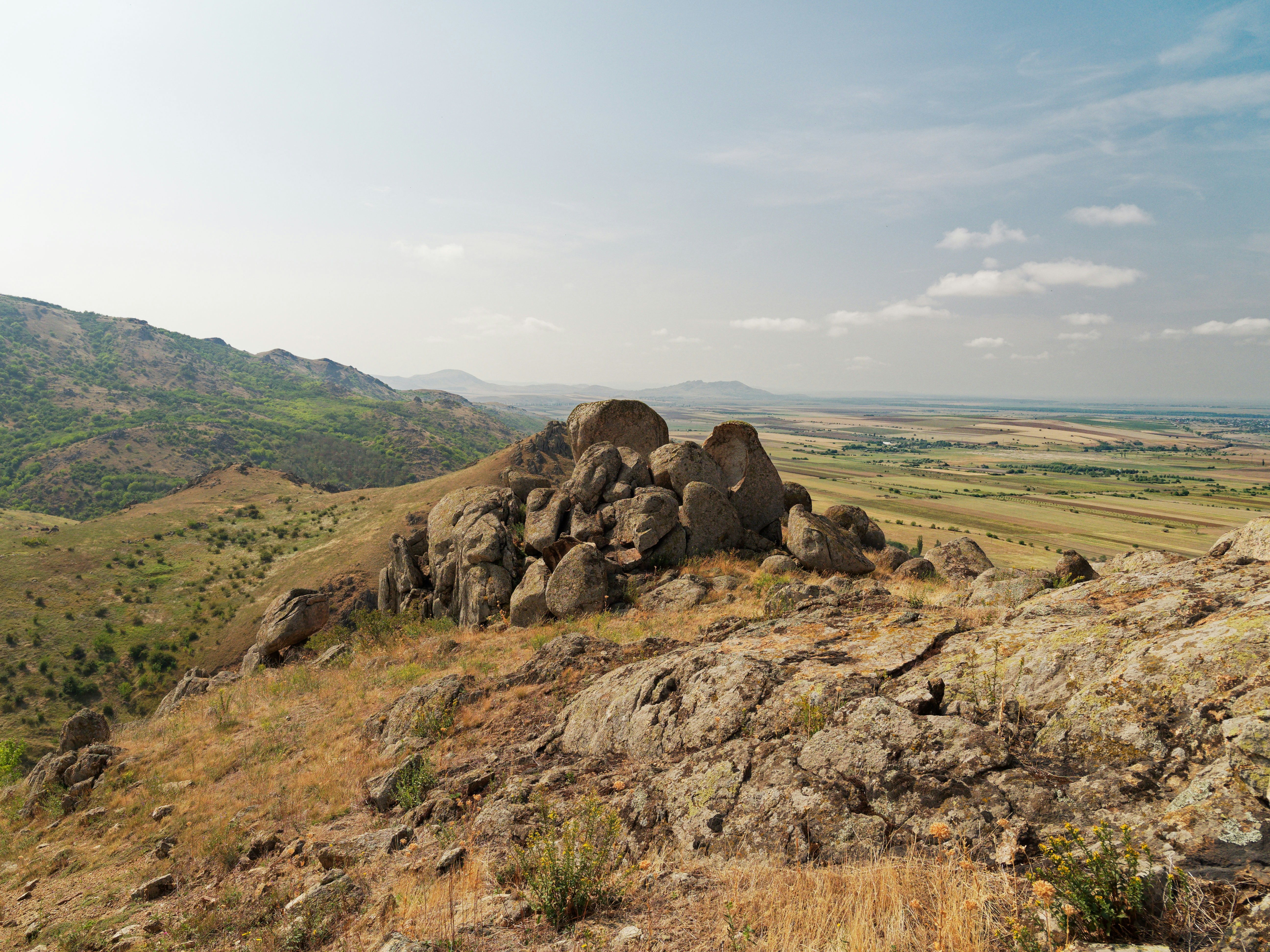 Rugged rocks stand sentinel over a sprawling valley, framed by distant mountains under a clear sky.