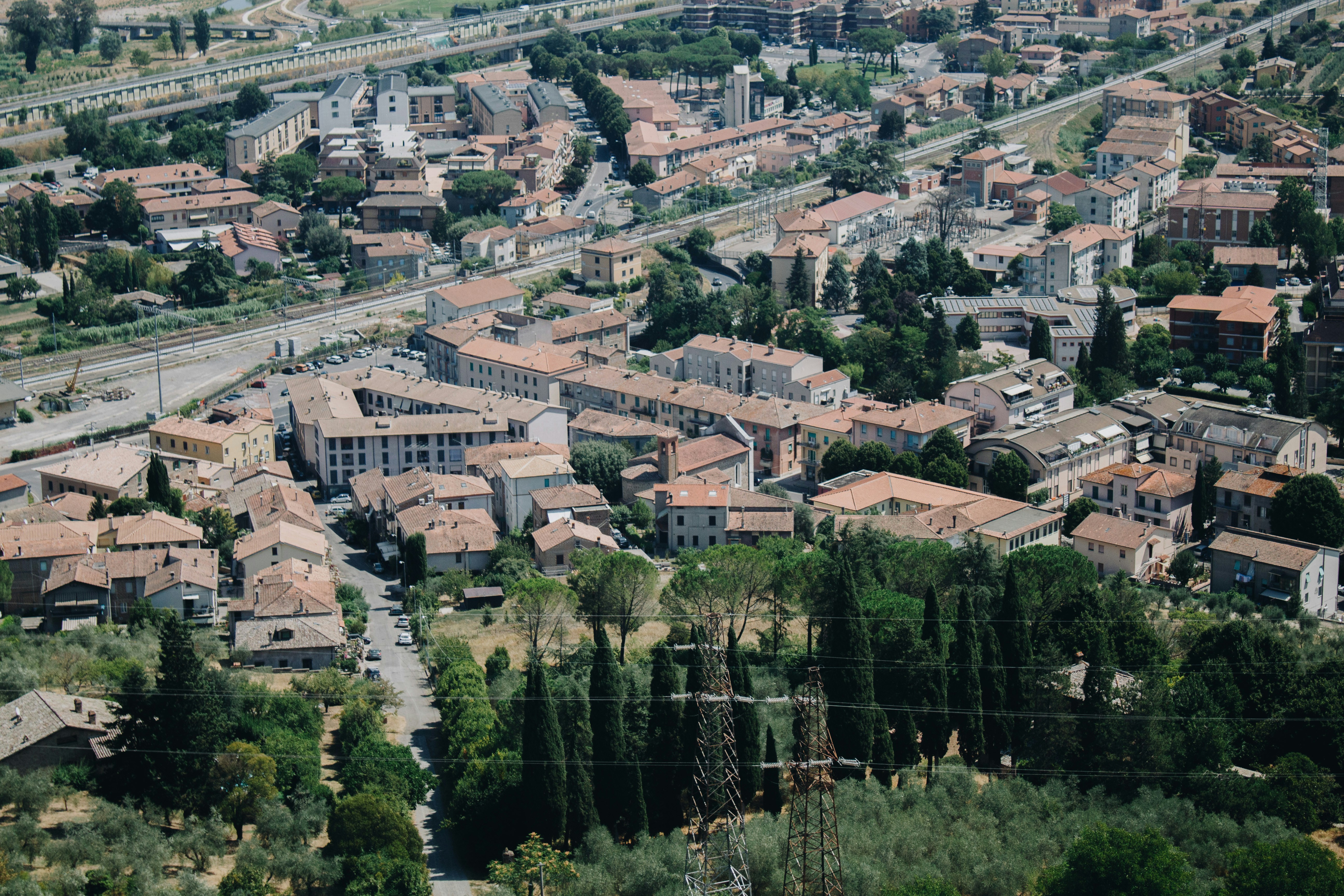 Aerial view of a quaint town showcasing terracotta rooftops and lush greenery, interspersed with winding roads and modern infrastructure.