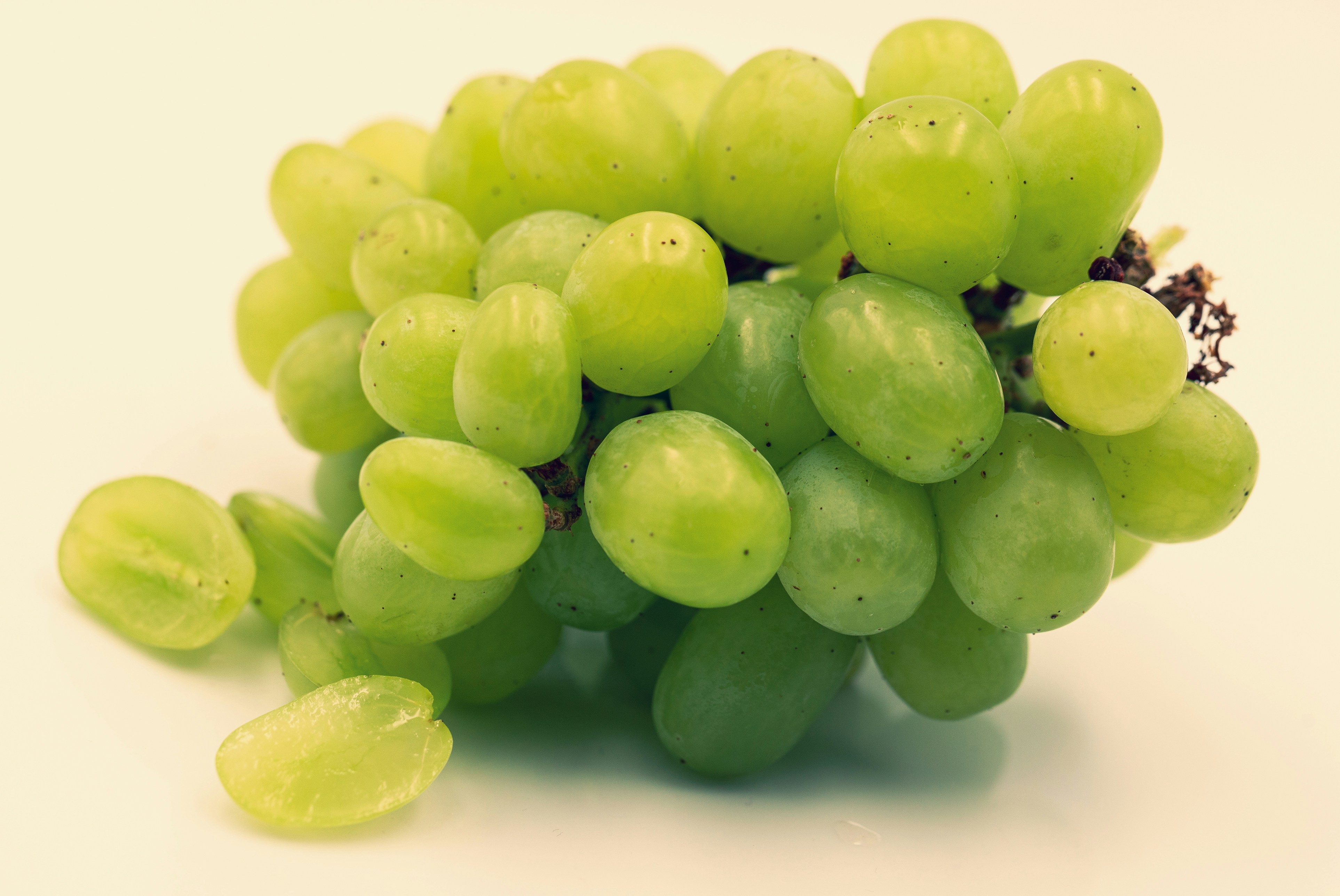 A close-up of a bunch of green grapes, showcasing their plump texture and subtle sheen against a light background.