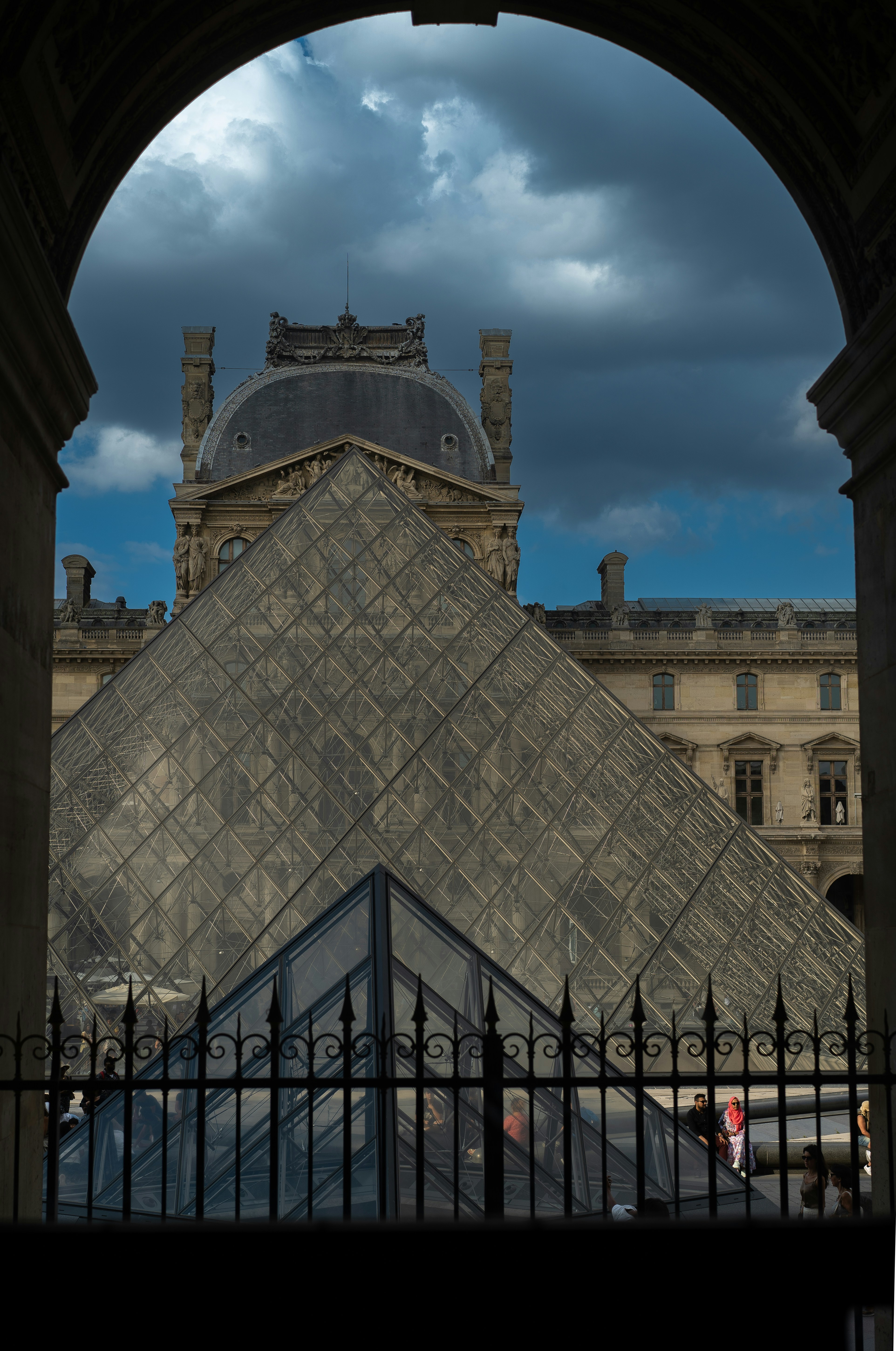 Stone-arch Framing: Louvre Pyramid Rising Under Brooding Skies