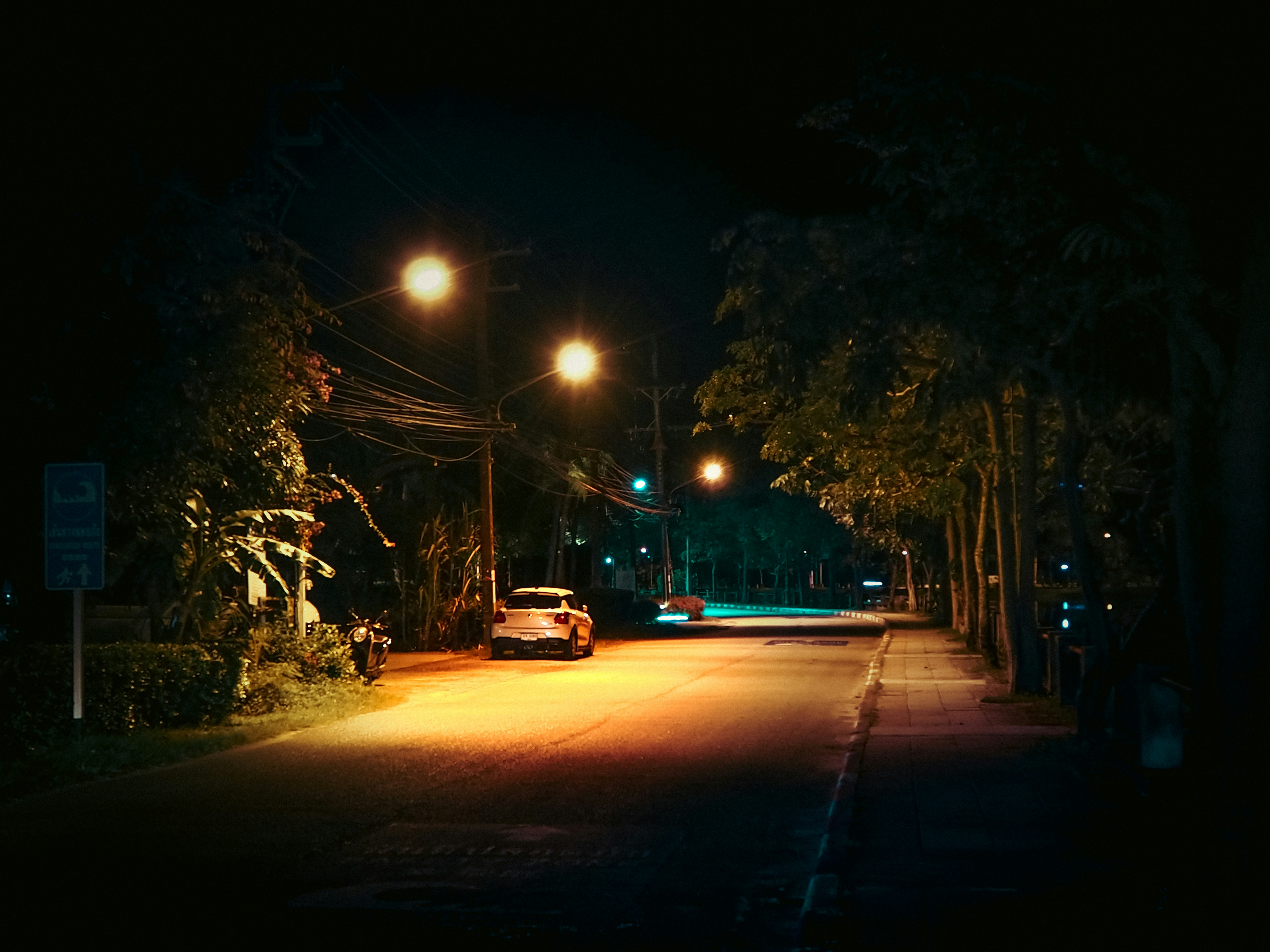 Dimly lit street lined with trees and streetlights, creating a serene nighttime atmosphere. A parked car adds to the tranquil scene.