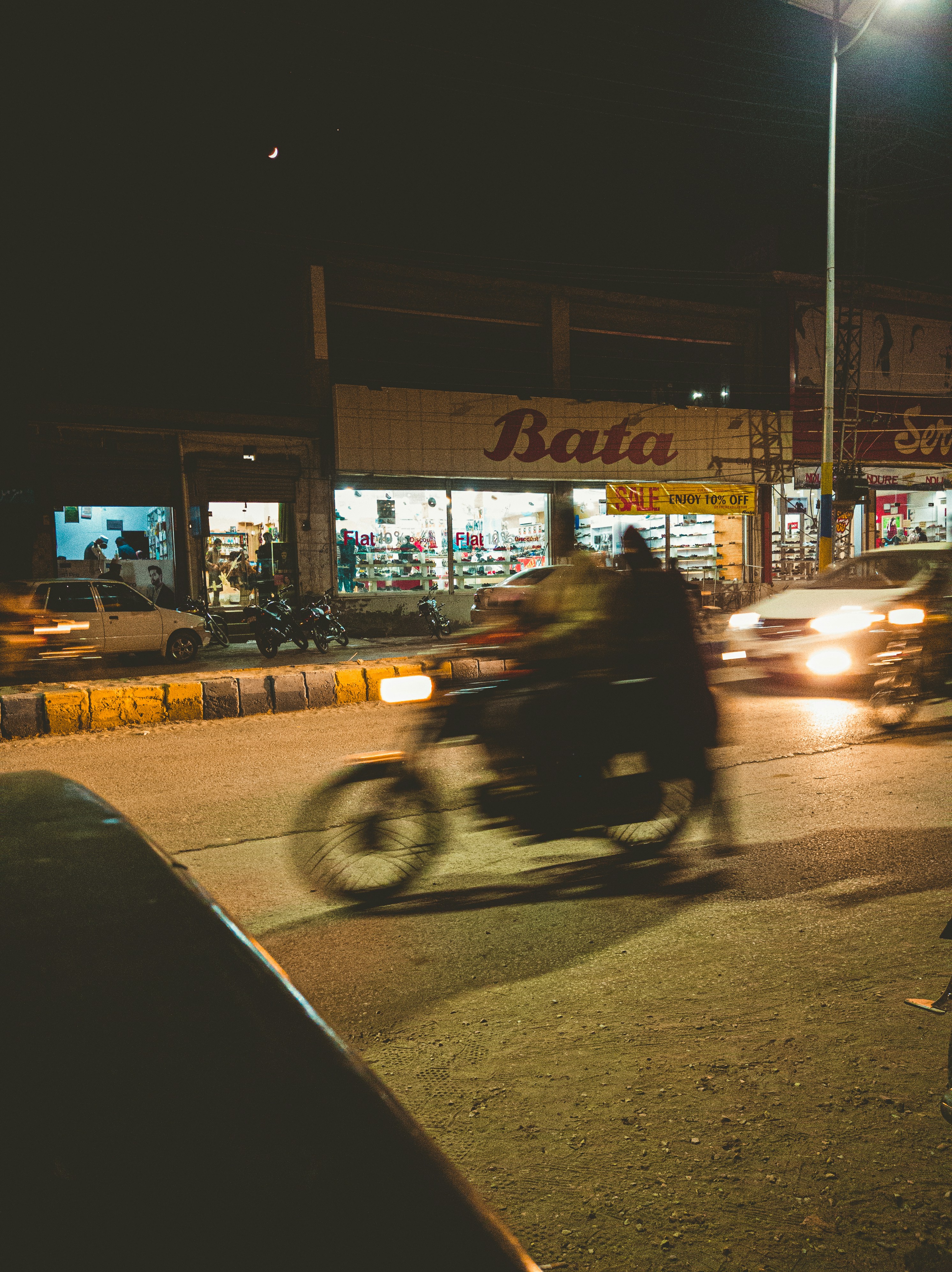 Motorcycle speeding through a dimly lit street with blurred motion against a backdrop of illuminated shop signs.