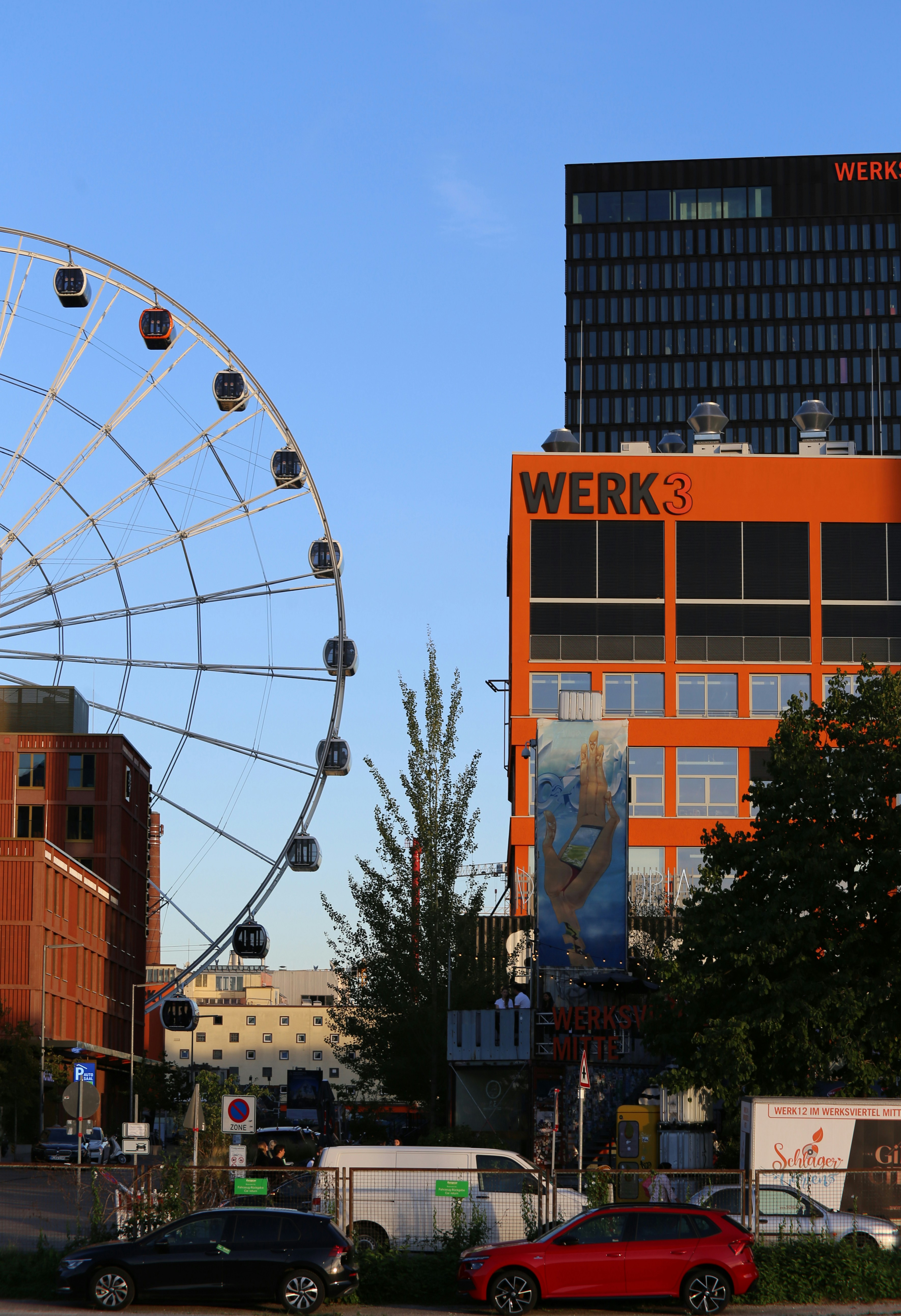 Werk3 in Orange: A City Block Framed by a Giant Ferris Wheel Under a Clear Blue Sky