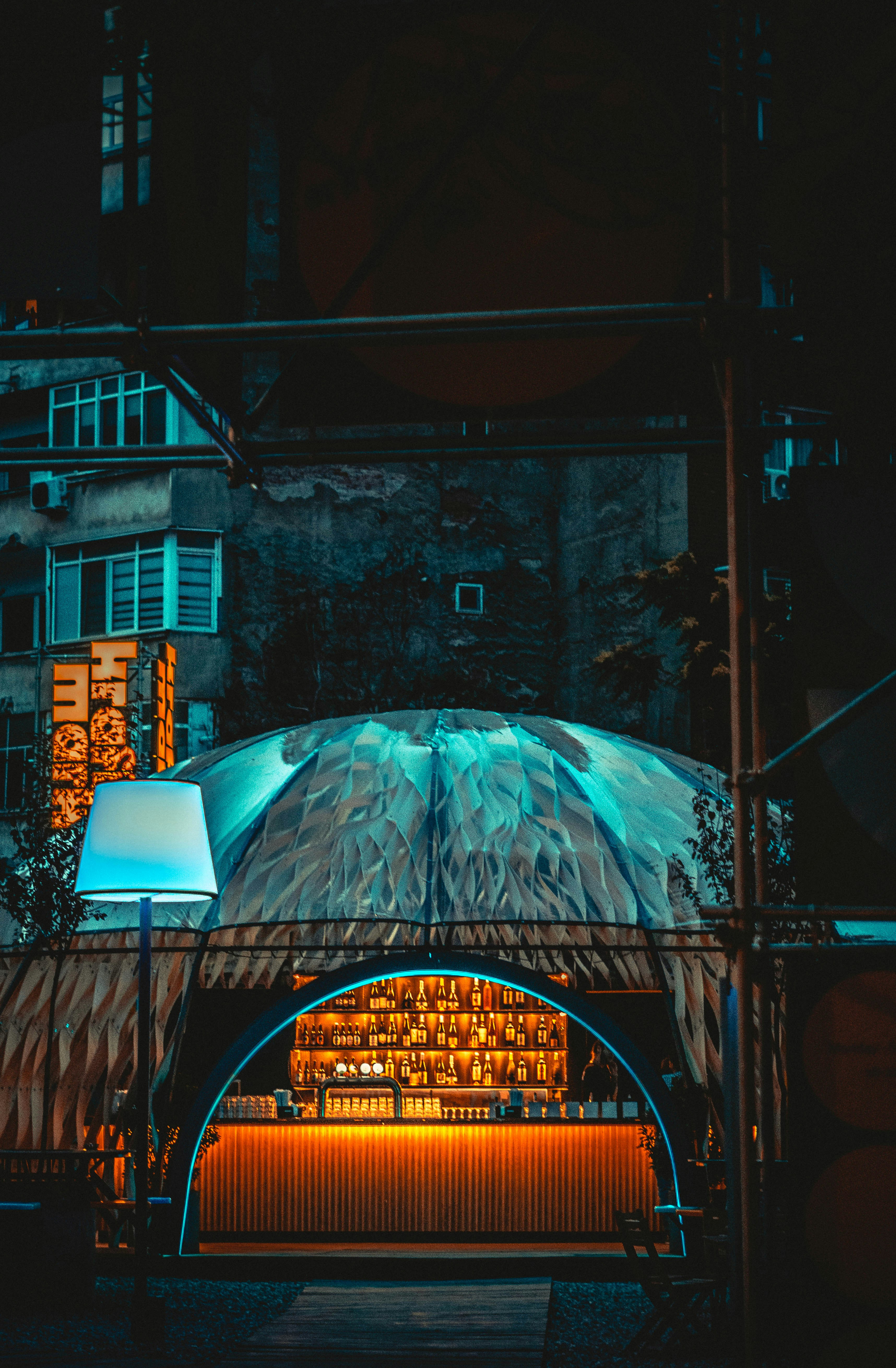 A modern bar with a distinctive dome structure, illuminated by warm lights, set against a dark urban backdrop. The scene captures a vibrant nightlife atmosphere.