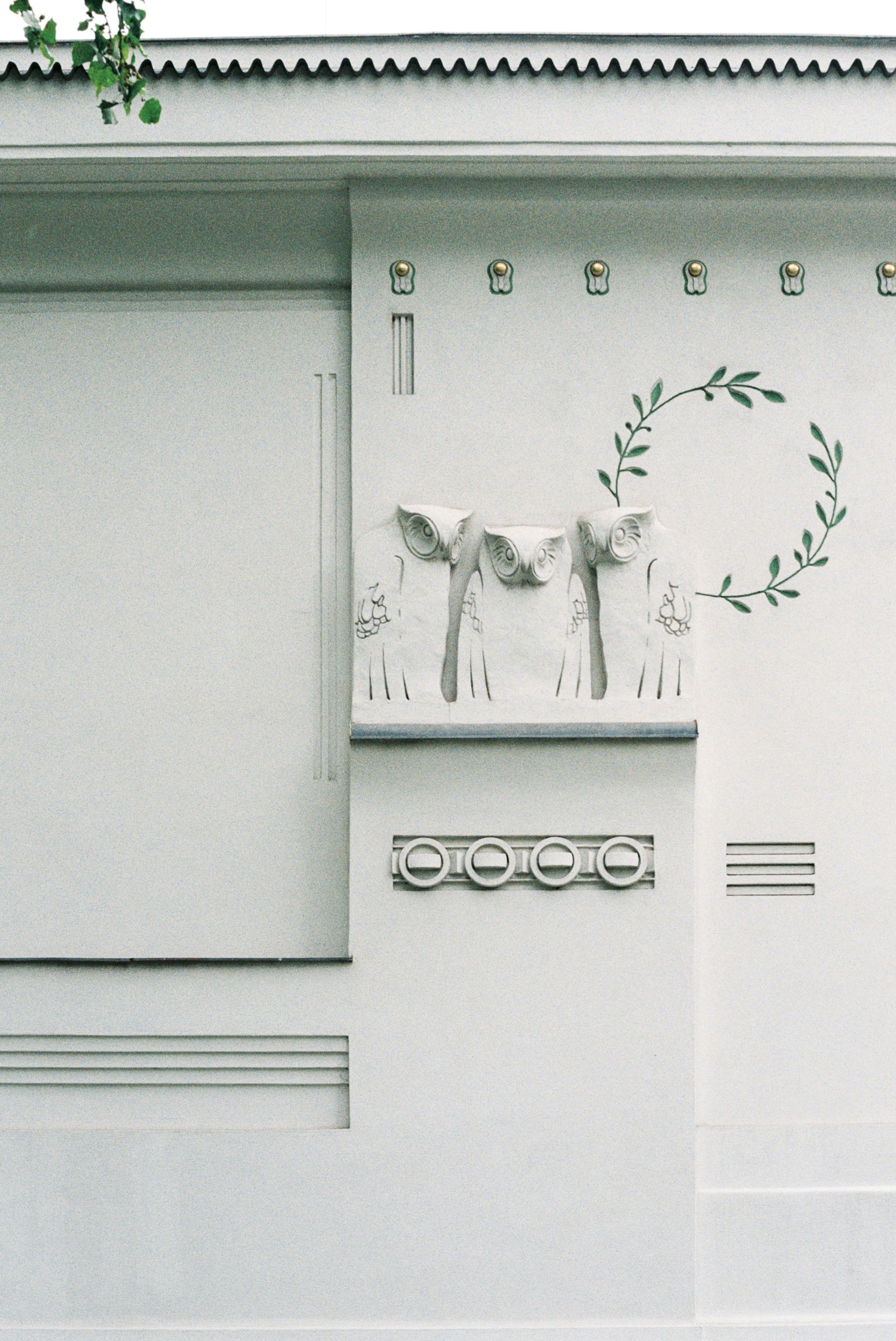 Intricate plasterwork featuring stylized eyes and delicate foliage on a minimalist wall, showcasing an artistic blend of form and texture.