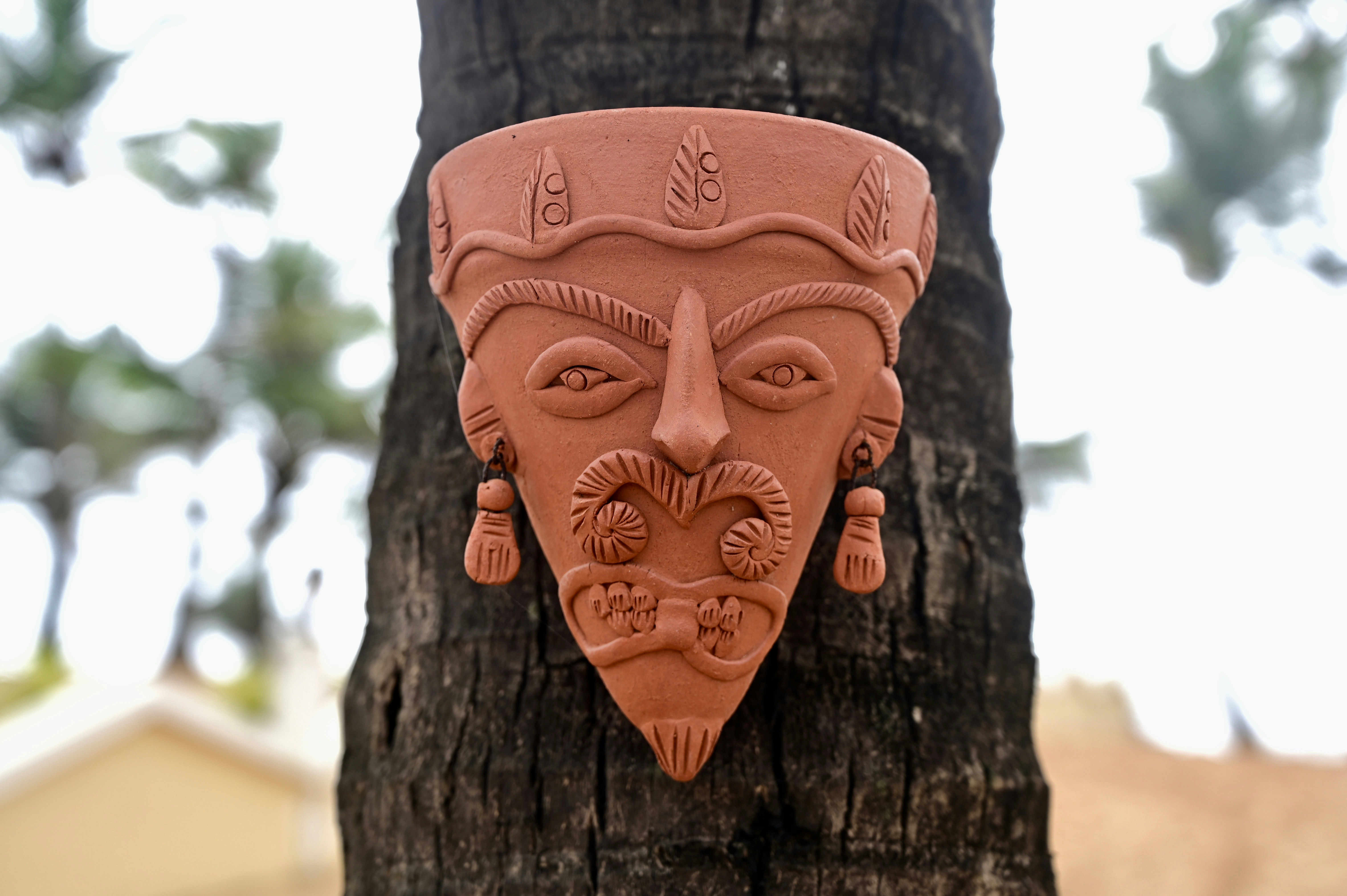 Terracotta Mask Adorned on a Tree Trunk: Quiet Portrait in a Sunny Yard