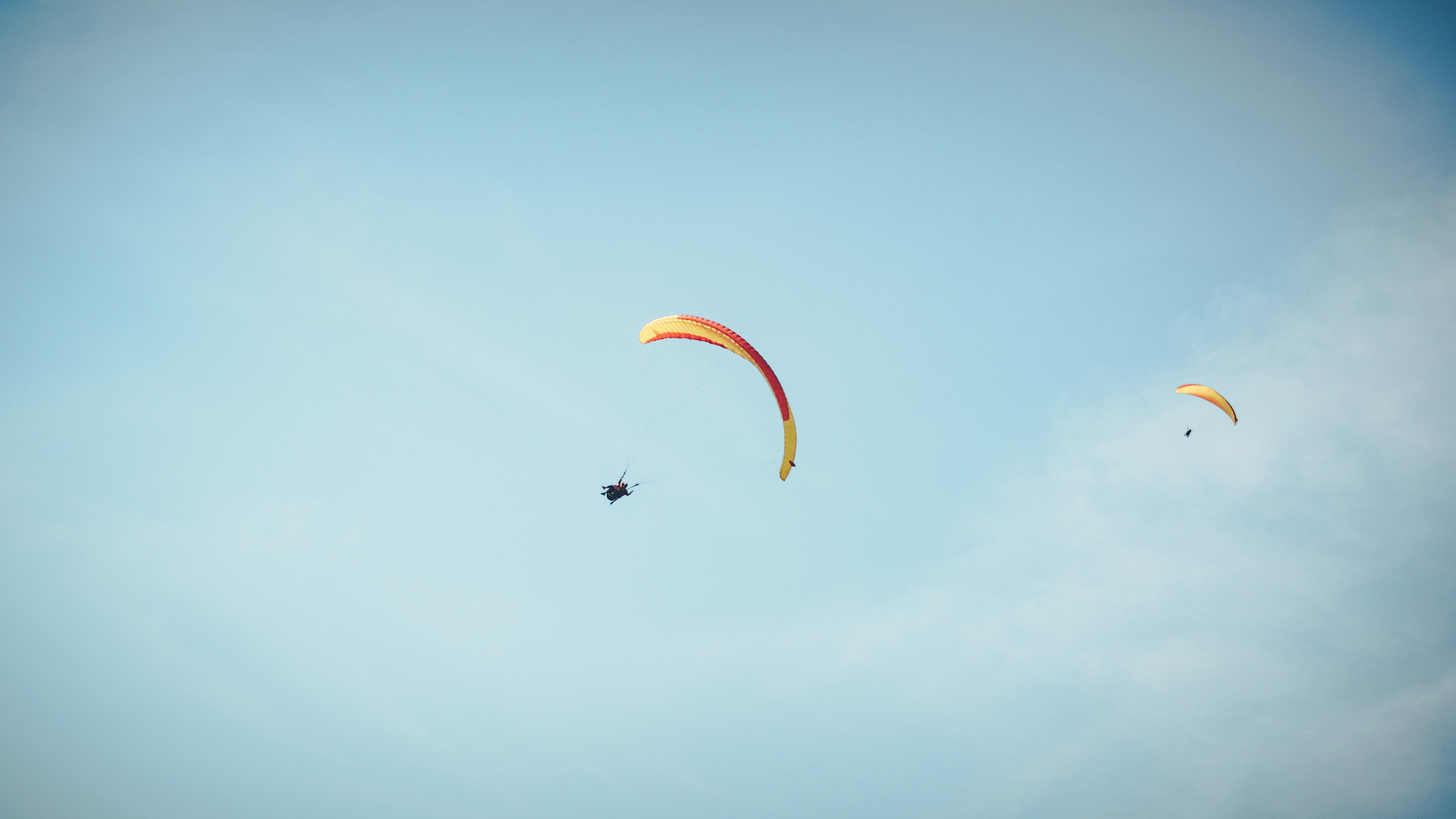 Two colorful paragliders gliding gracefully against a clear blue sky, showcasing the thrill of aerial adventure.