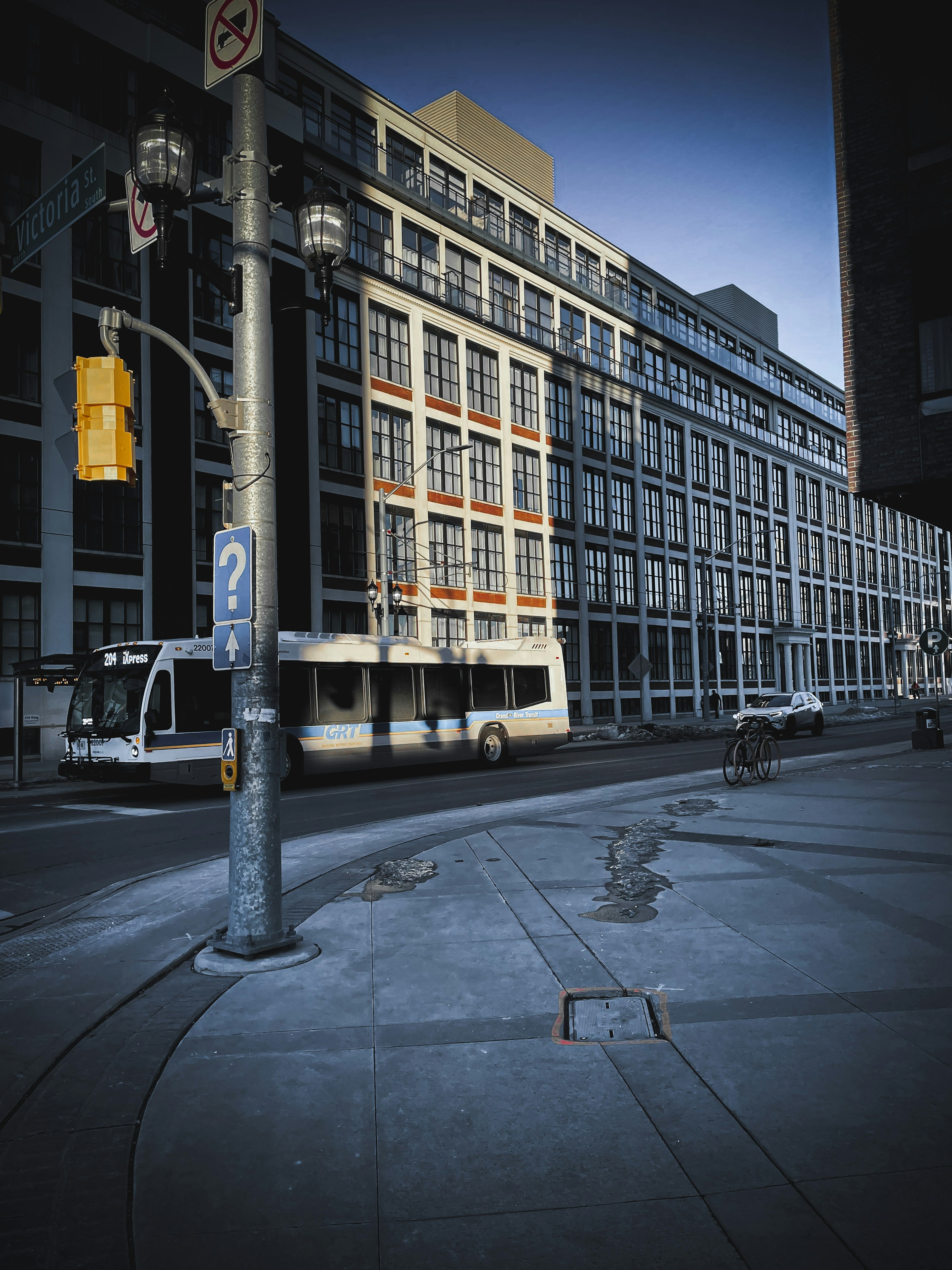 City bus traversing a wide street with a modern building backdrop under a clear sky.