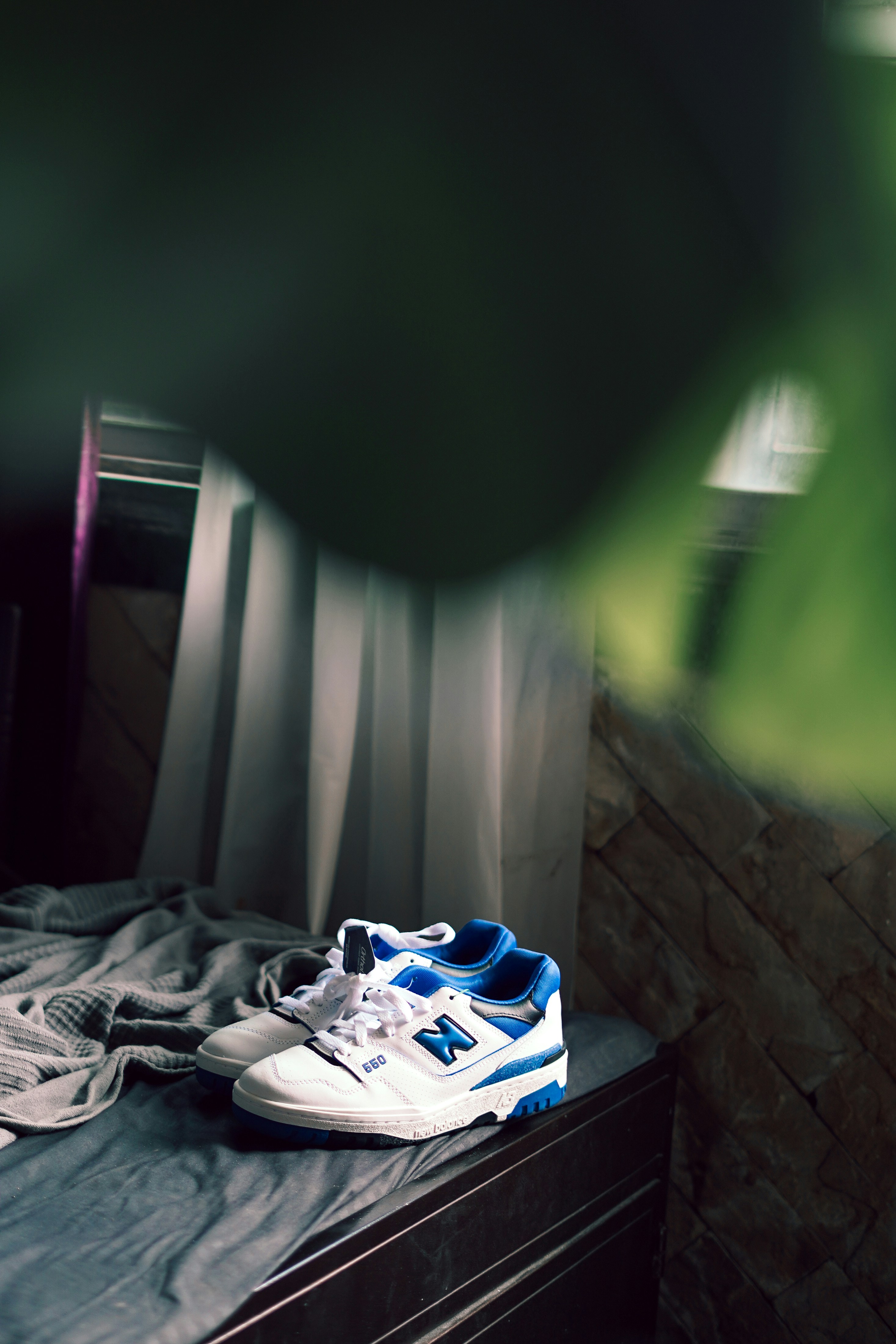 Blue-Trim Sneakers Grounded on a Dim Surface Beneath a Draped Curtain