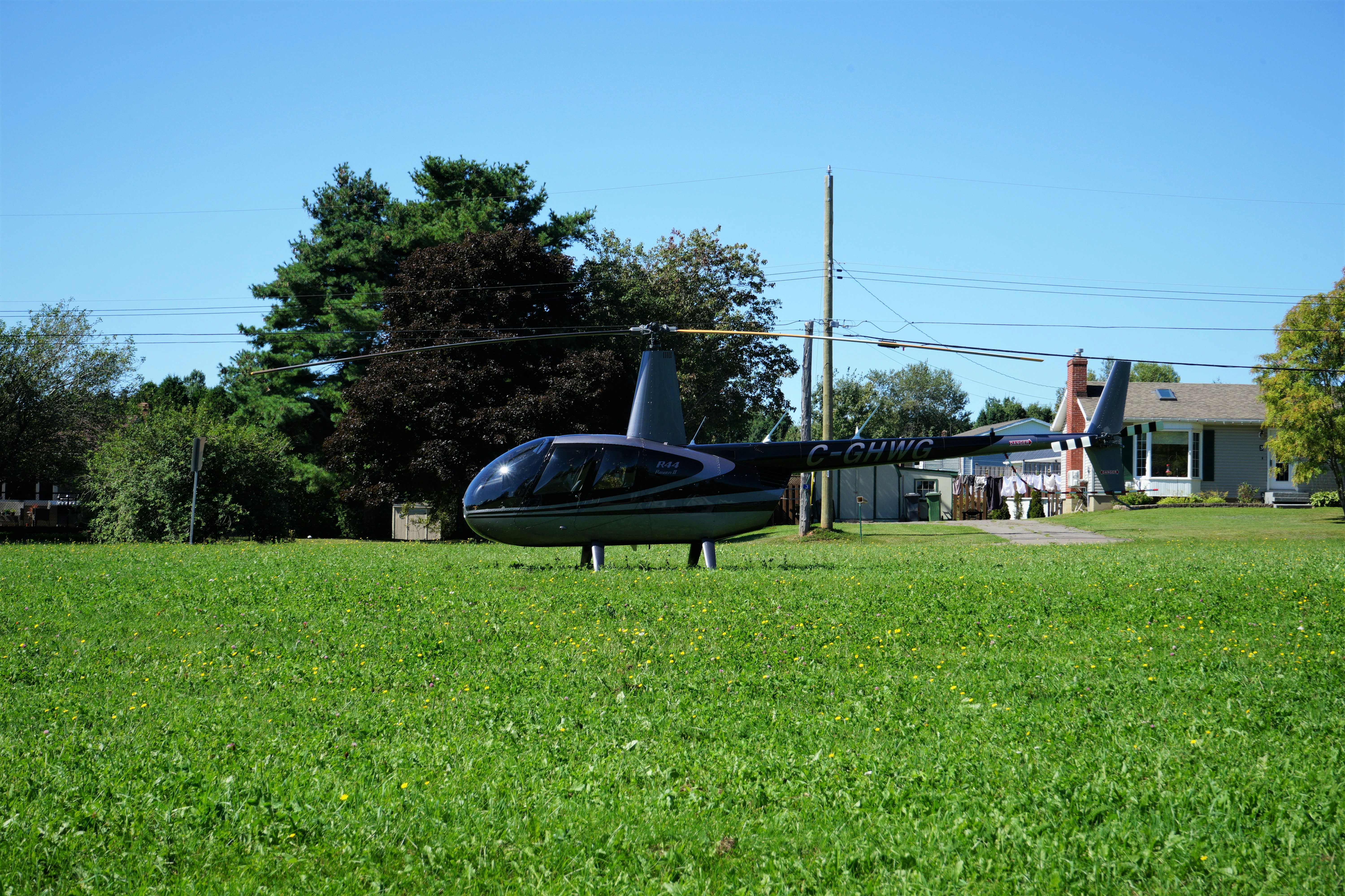 A sleek helicopter parked on a lush green lawn, surrounded by trees and a residential home in the background.