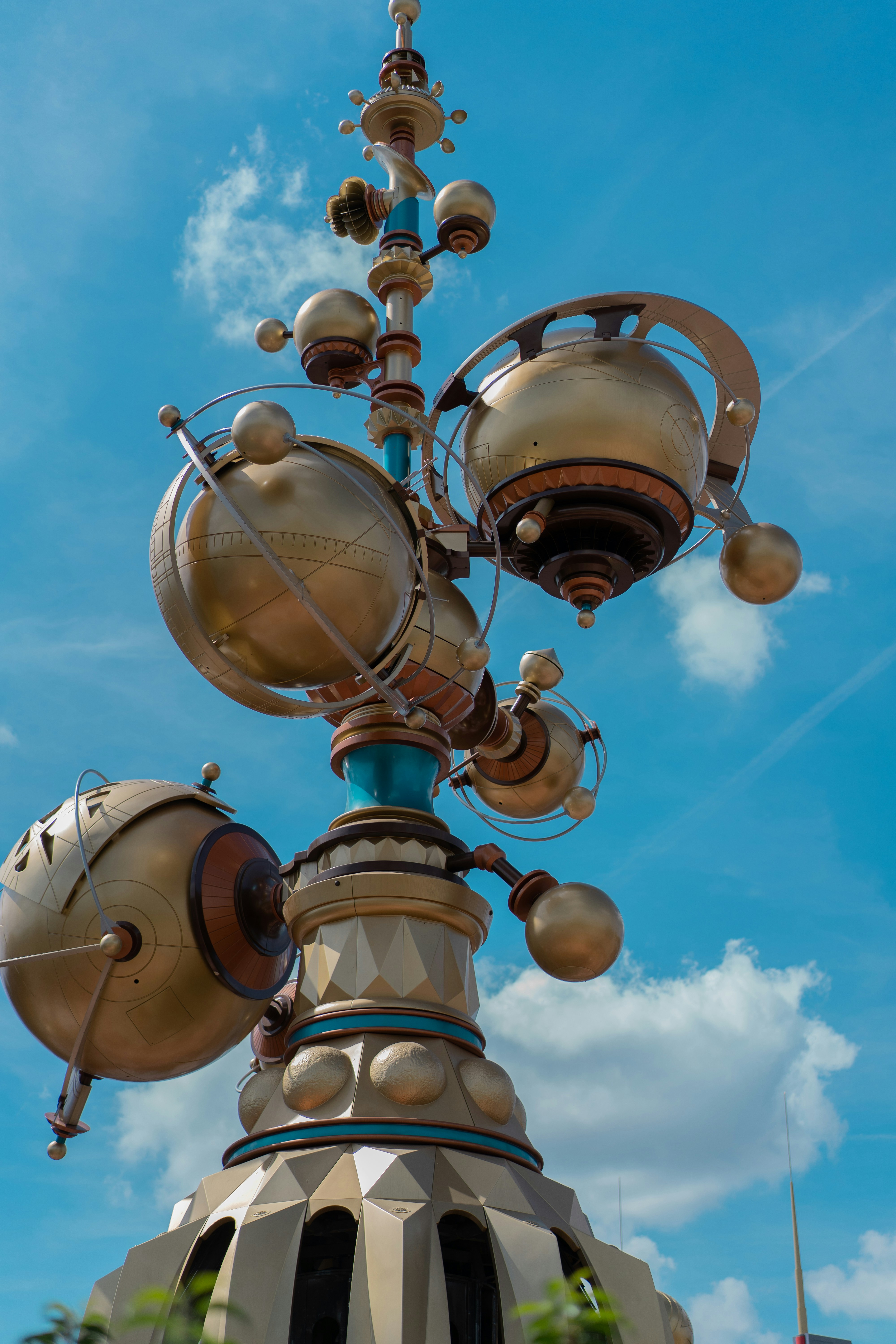 Sculptural tower of metallic spheres and rings reaches toward a blue sky, emphasizing industrial precision and geometric forms.