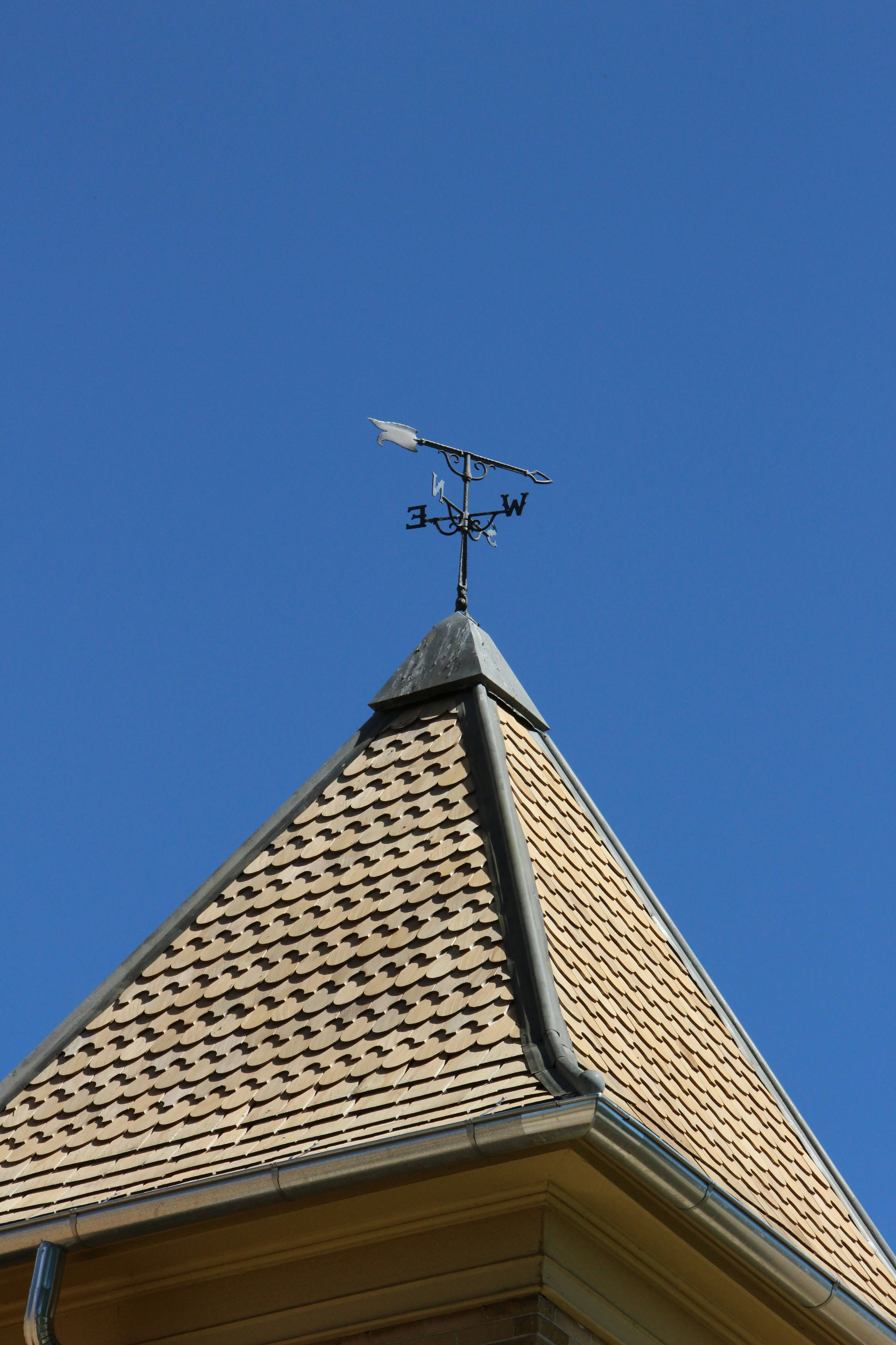 Weather Vane Crowned on a Terracotta Roof Under a Pristine Blue Sky