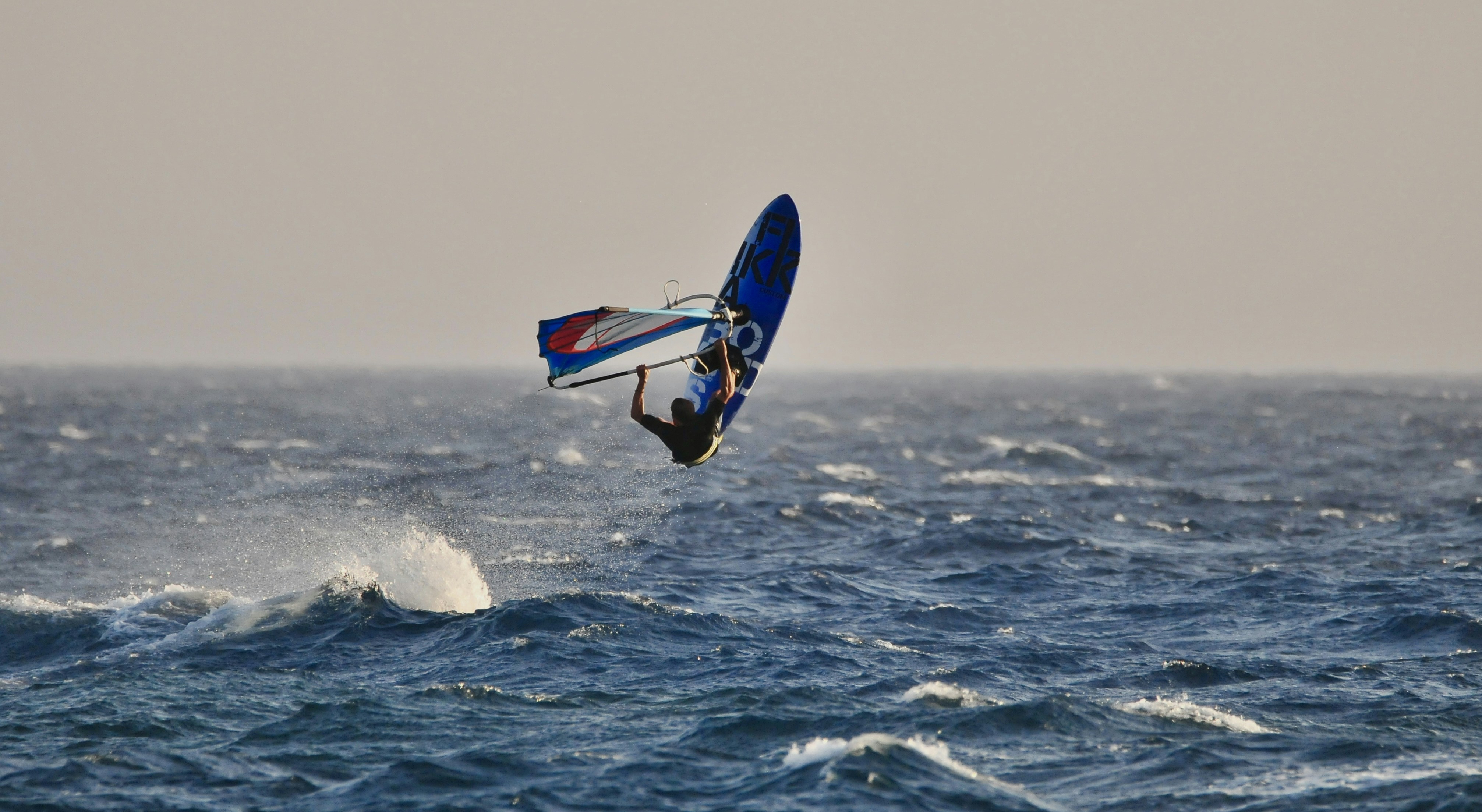 Windsurfer executing a dynamic aerial maneuver above the ocean surface, showcasing skill and agility amidst choppy waters.